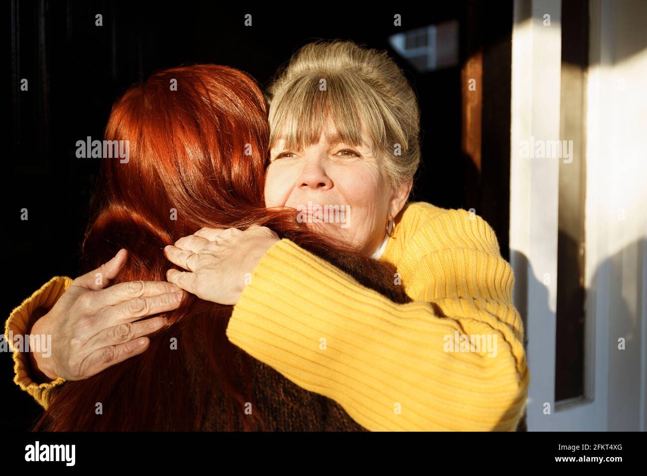 Rear view of senior woman and adult daughter hugging at front door ...