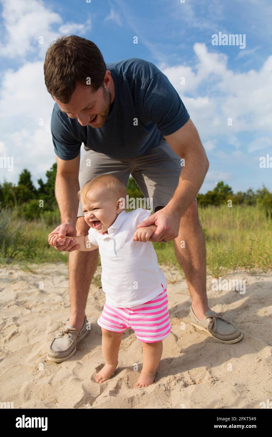 Mid adult man holding baby daughters hands while toddling in sand Stock ...