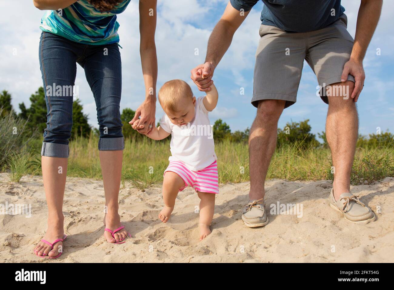 Mid adult parents holding baby daughters hands while toddling in sand ...