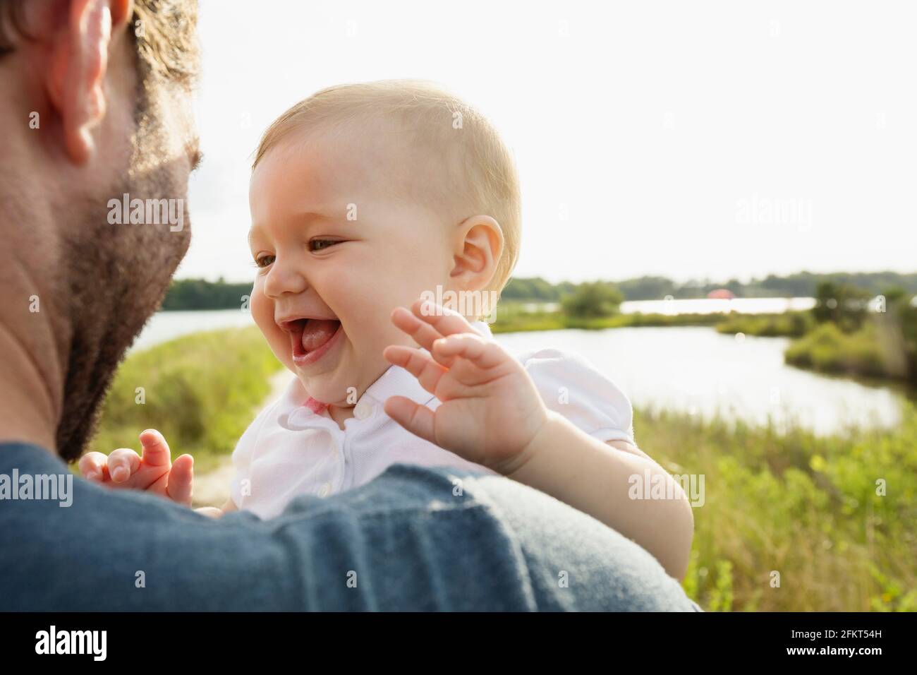 Over shoulder view of mid adult man carrying baby daughter on riverside ...
