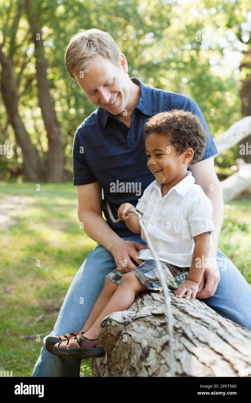 Father and son sitting on log holding twig smiling Stock Photo - Alamy