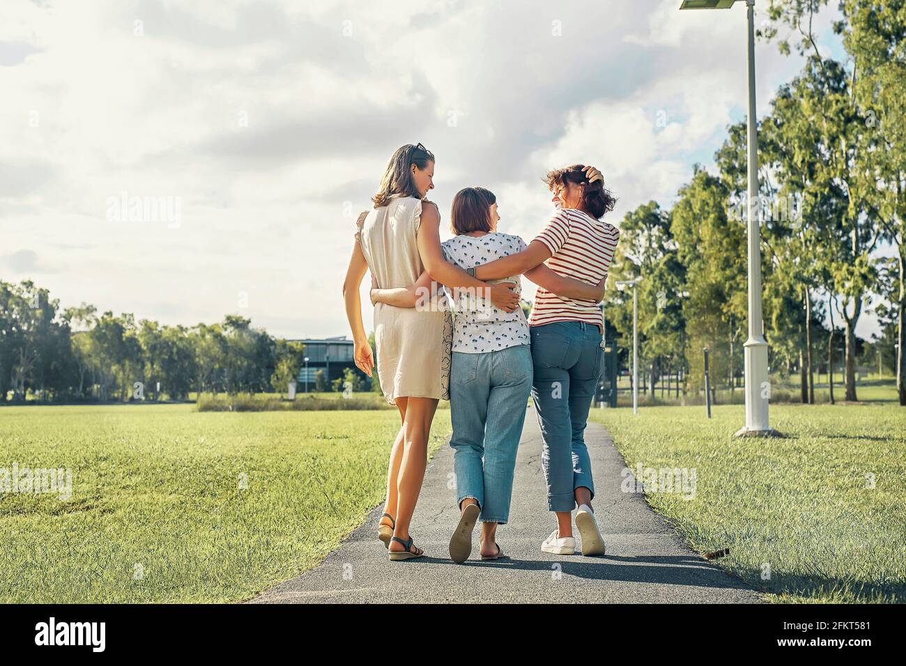 Three women friends with happiness emotion walking in the park hugging ...