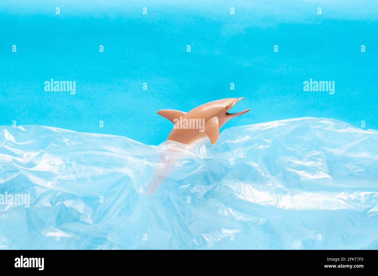 A dolphin toy model trapped in white plastic bag on blue background ...