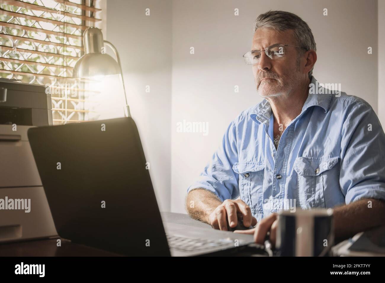 A senior man sitting at a desk in front of a laptop computer Stock ...