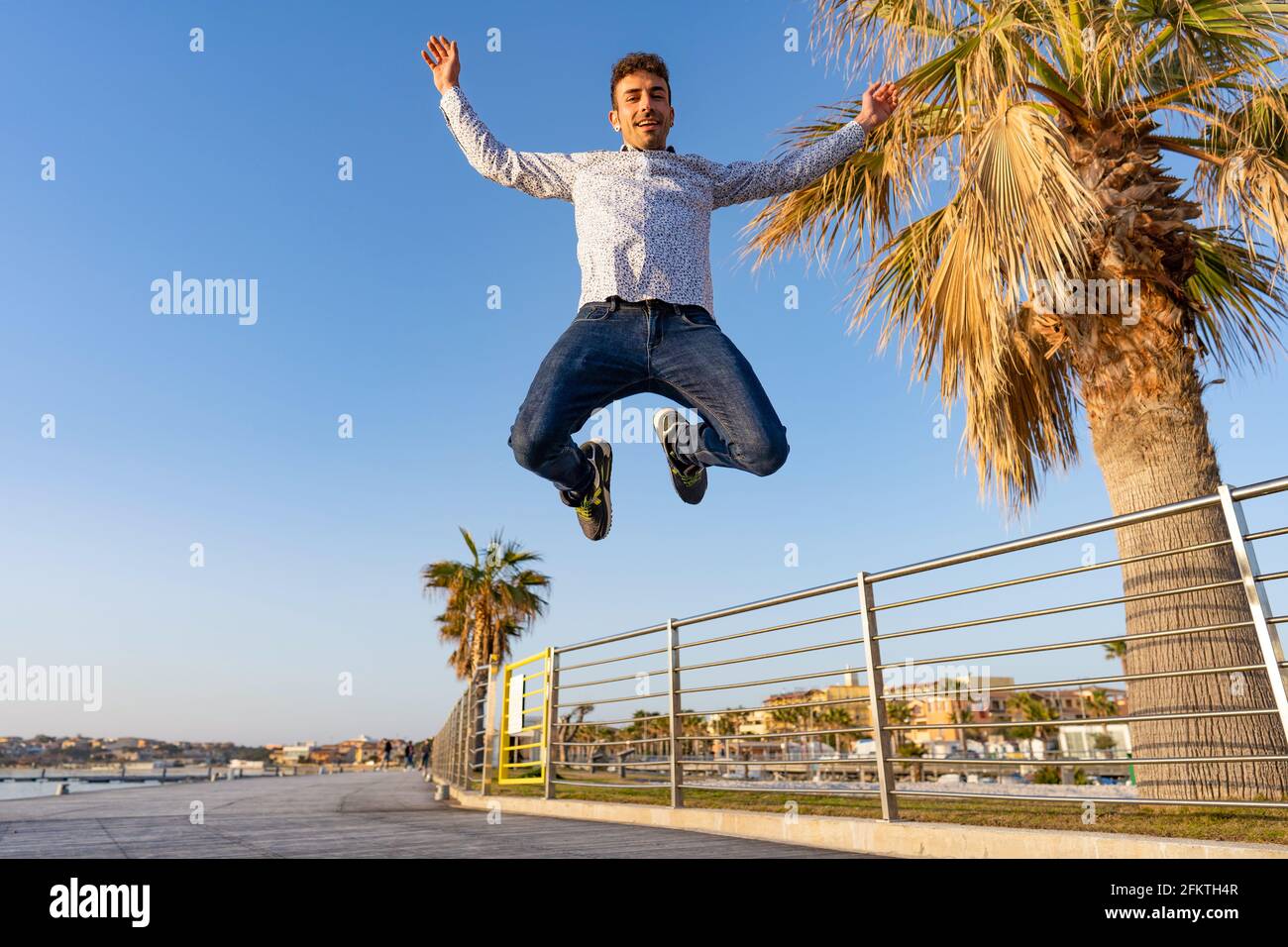 Happy boy jumping high with open arms looking at camera thinking about ...