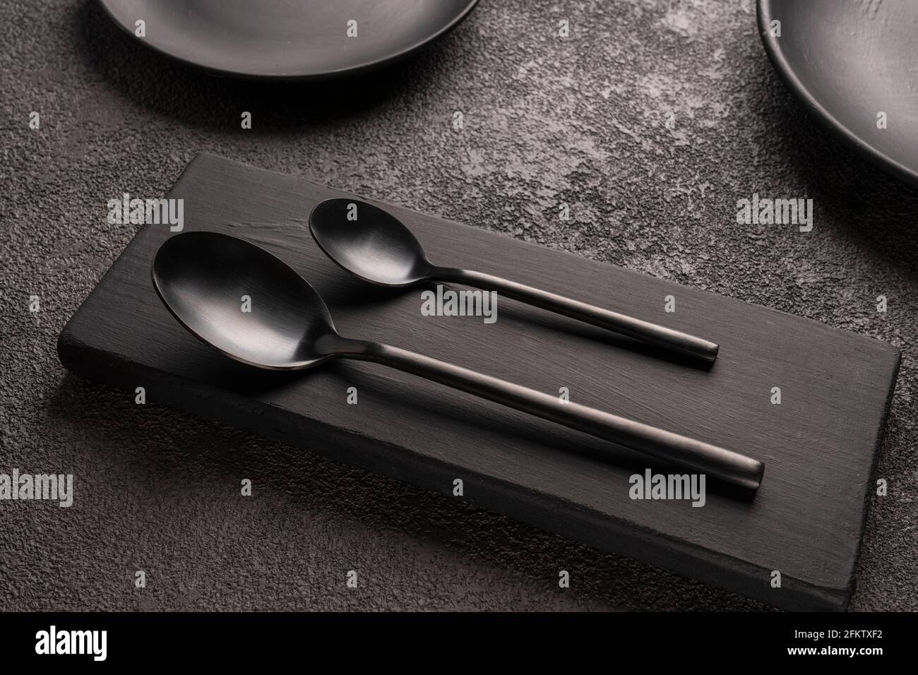 matte black spoons and surrounded by plates and utensils on a dark ...