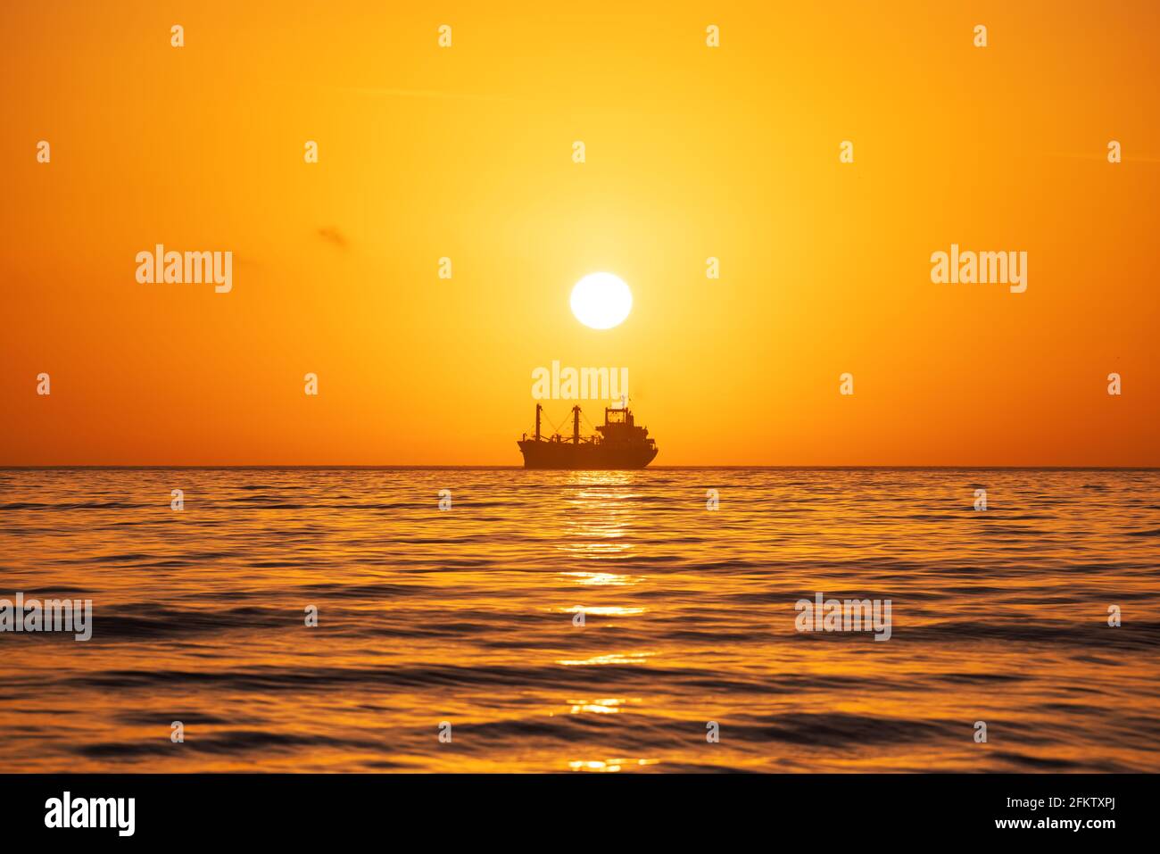 Sun setting at the sea with sailing cargo ship, scenic view Stock Photo ...
