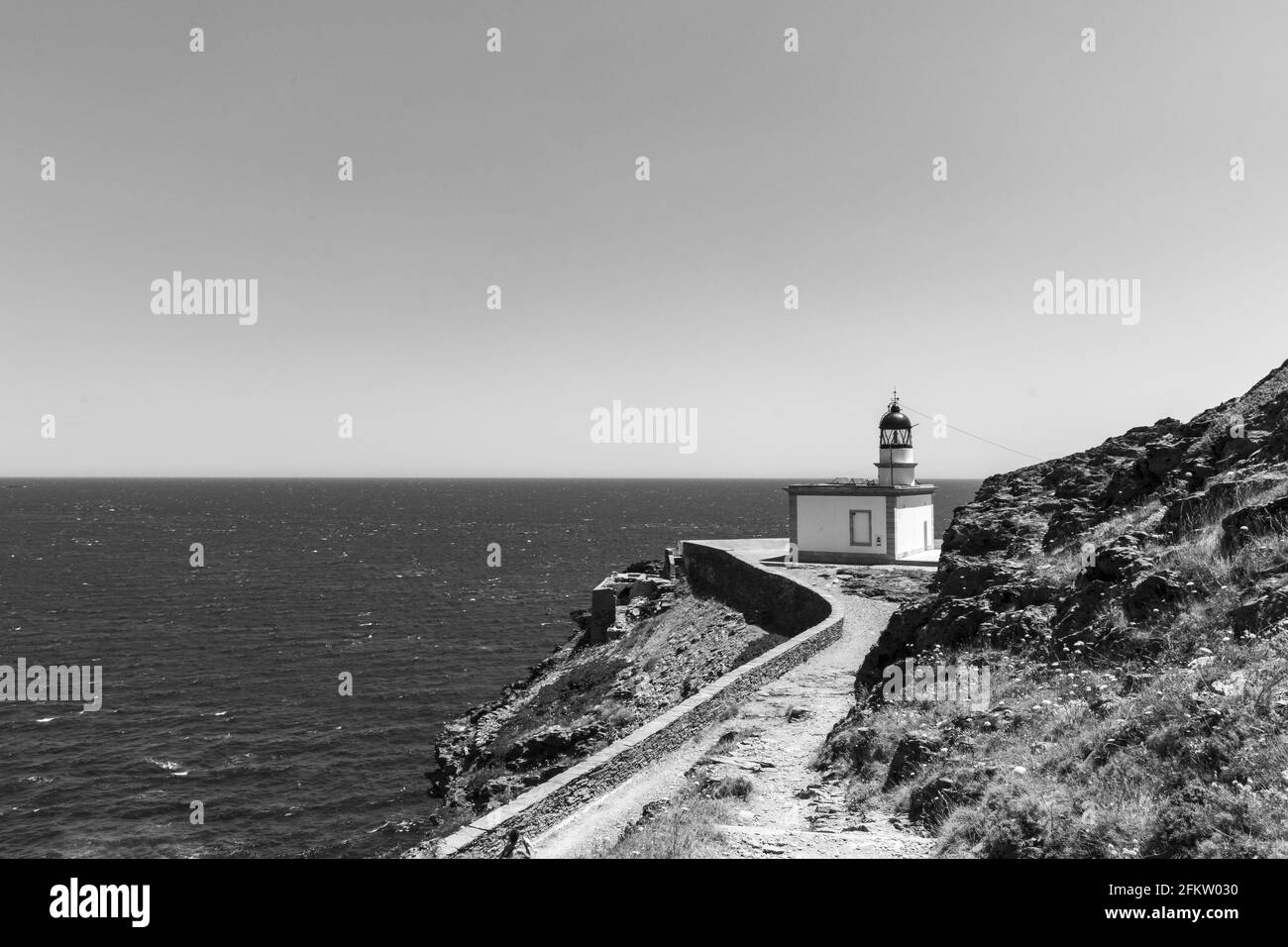 Grayscale shot of a lighthouse on a cliffy shore with the ocean in the ...