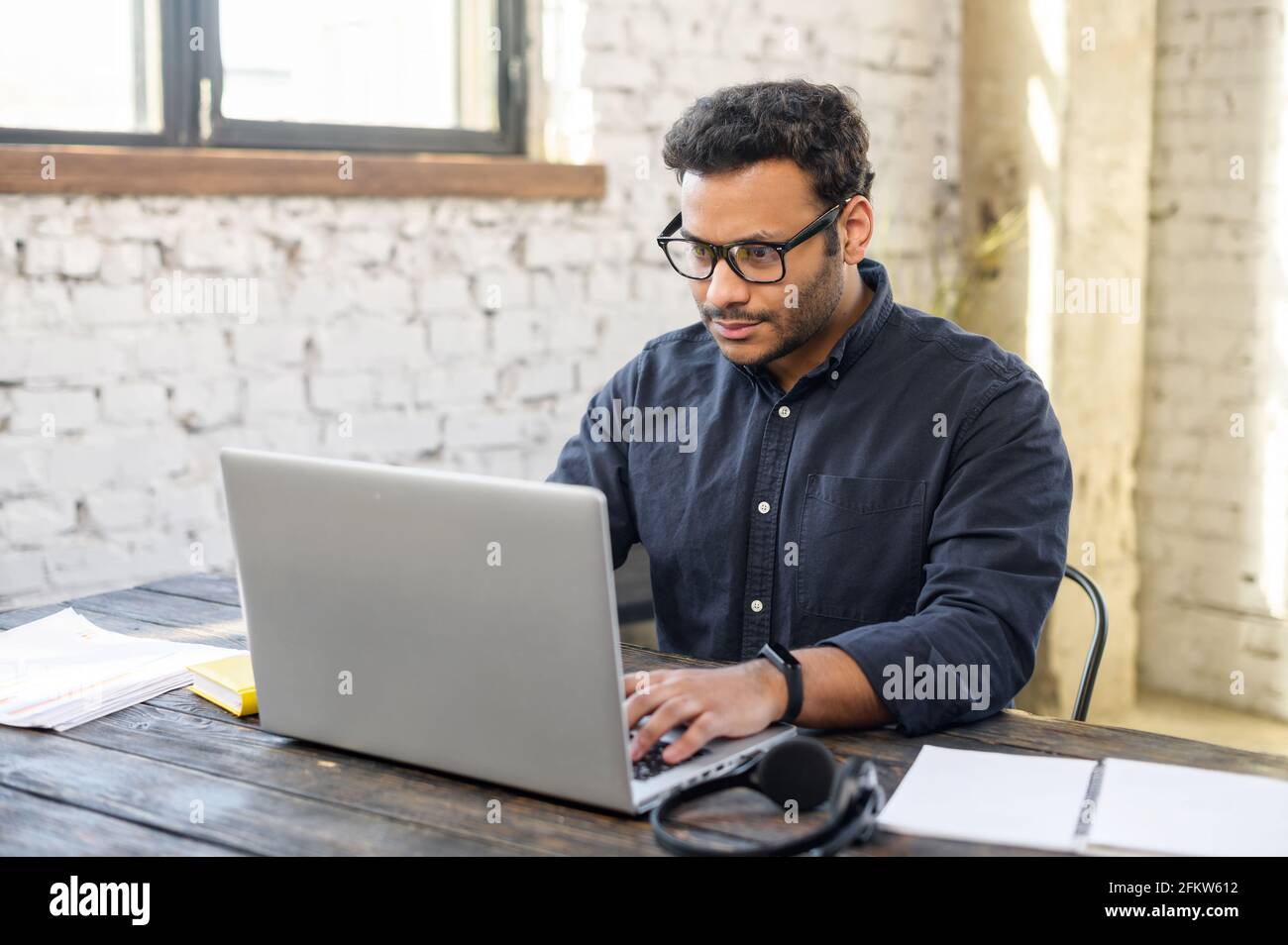 Focused hindu freelancer guy wearing eyeglasses using laptop in ...