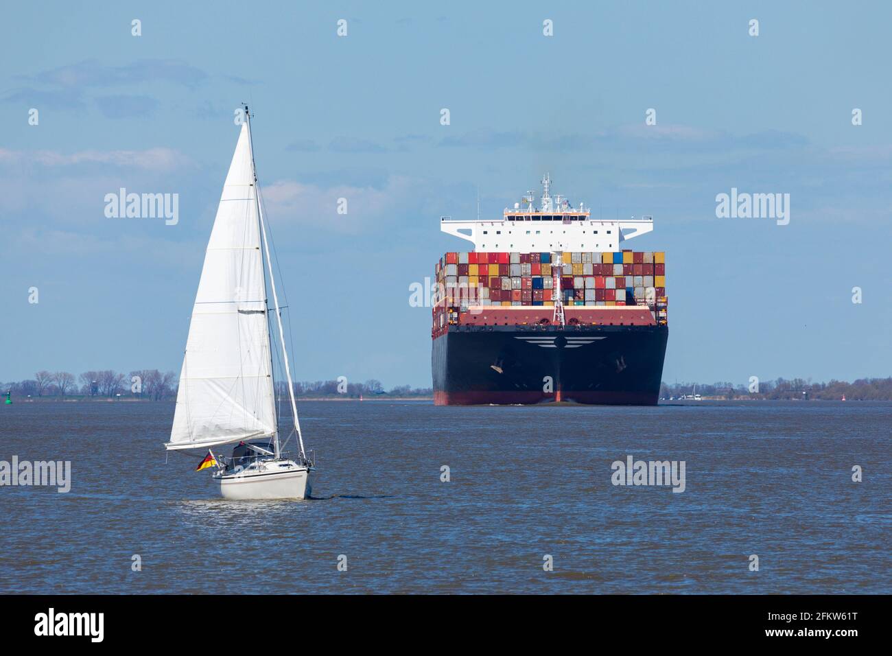 Small sail boat cruising in front of a huge container vessel on Elbe ...