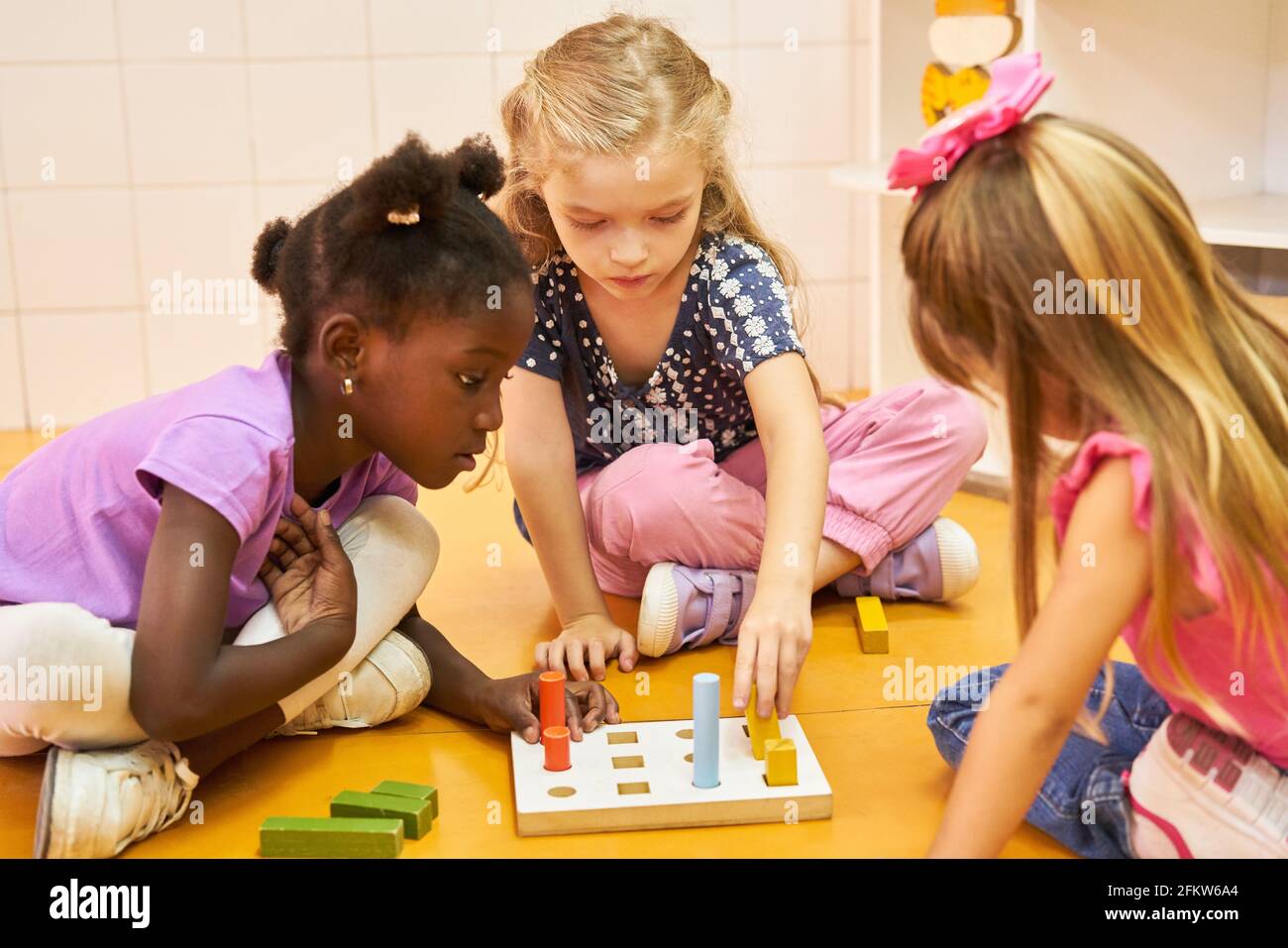 Multicultural children play a pegging game with blocks in an ...