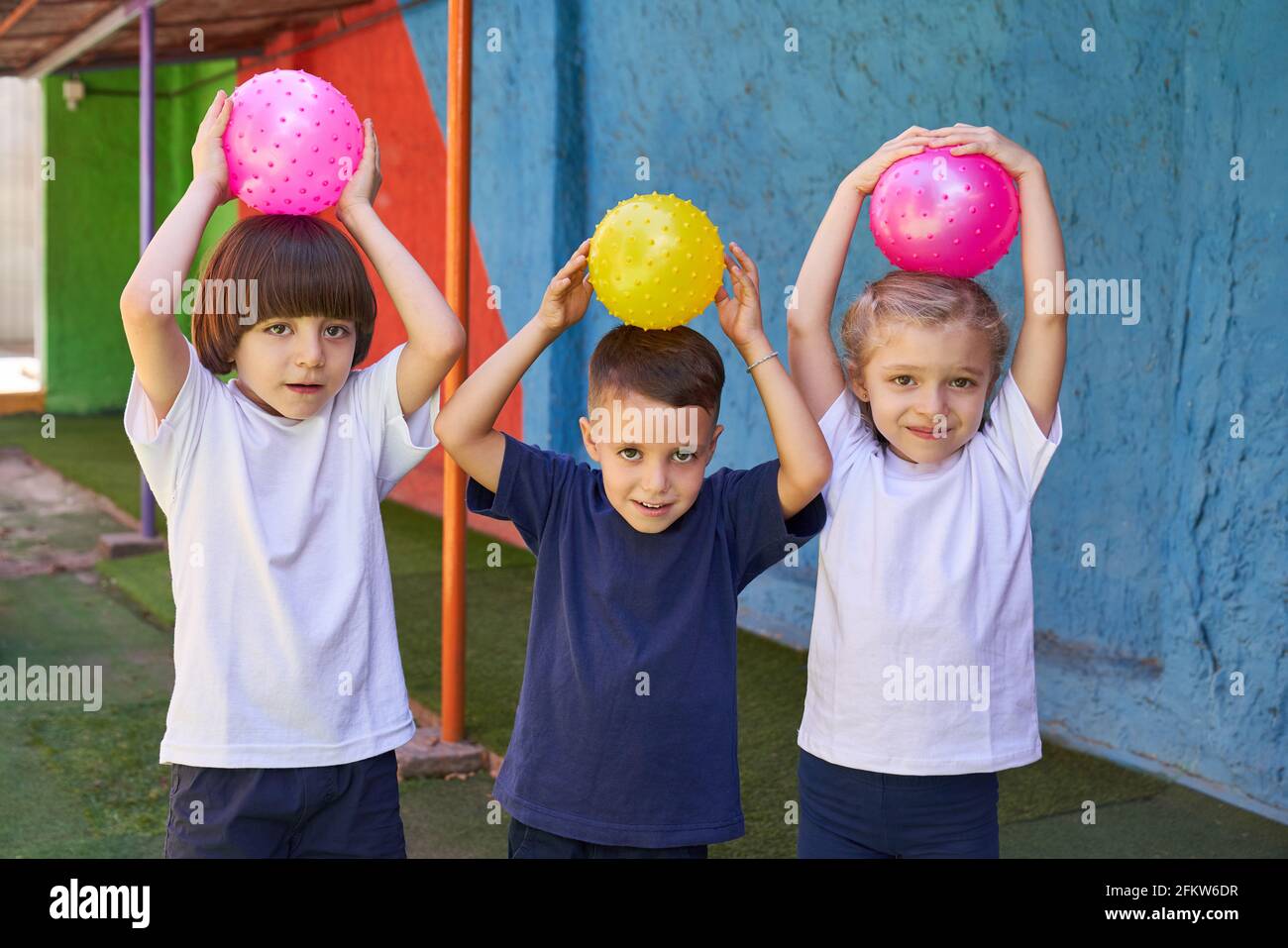 Three children as friends playing ball on the sports field in daycare ...