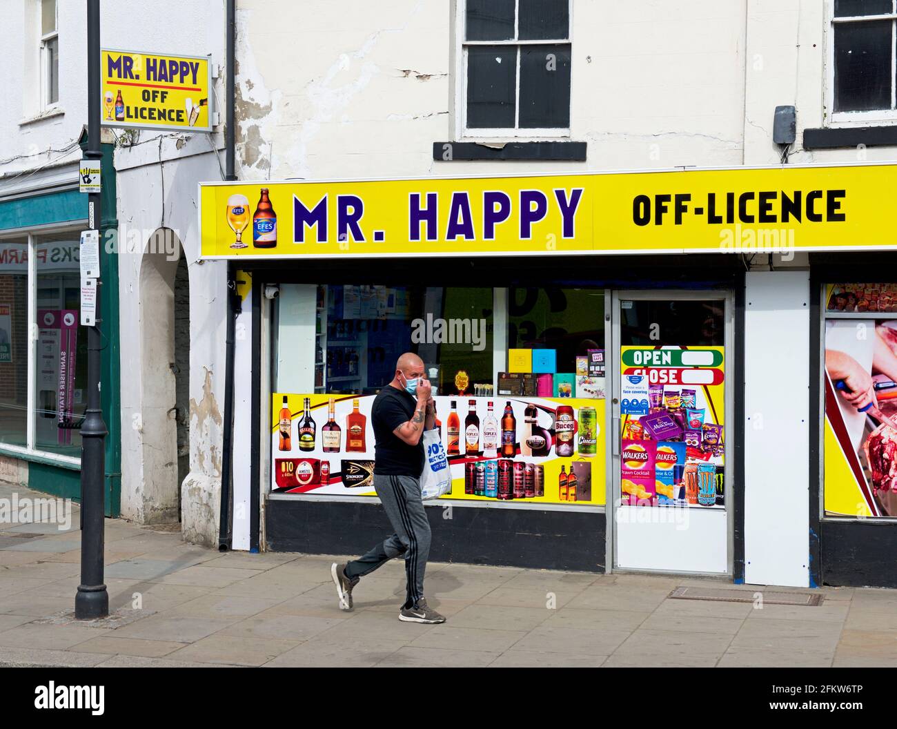 Man walking past shop - Mr Happy off-licence - in Thorne, South ...