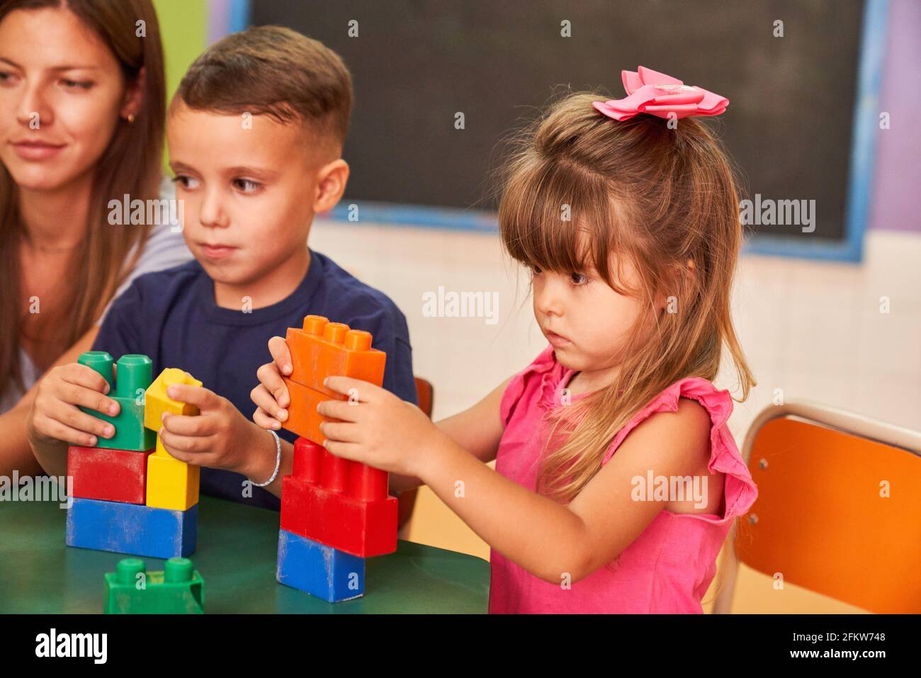 Little girl plays with colorful building blocks in kindergarten or ...