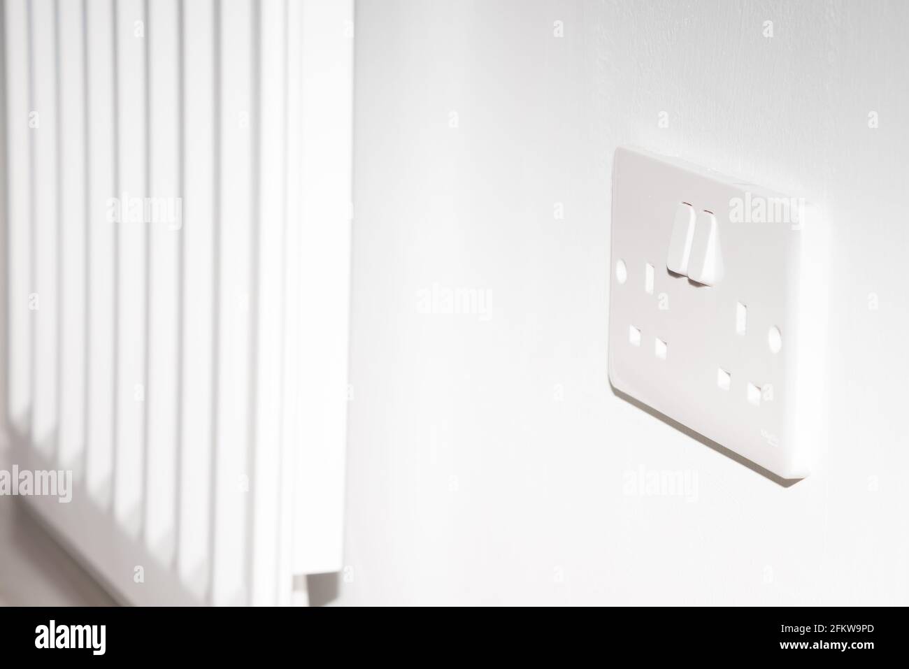 A United Kingdom standard wall socket on a white wall next to radiator ...