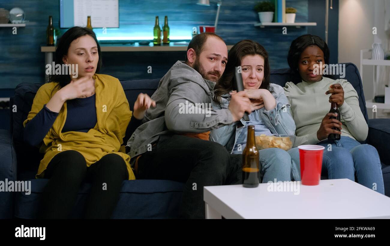 Multi-racial scared friends watching horror movie on television while ...