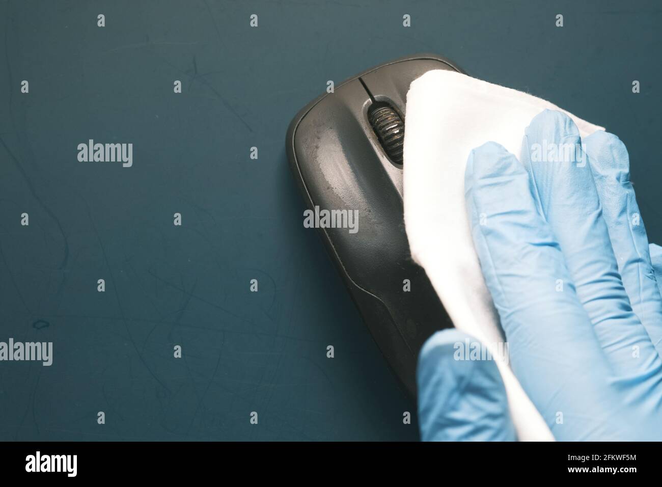 hand in blue rubber gloves and white tissue disinfecting computer mouse ...