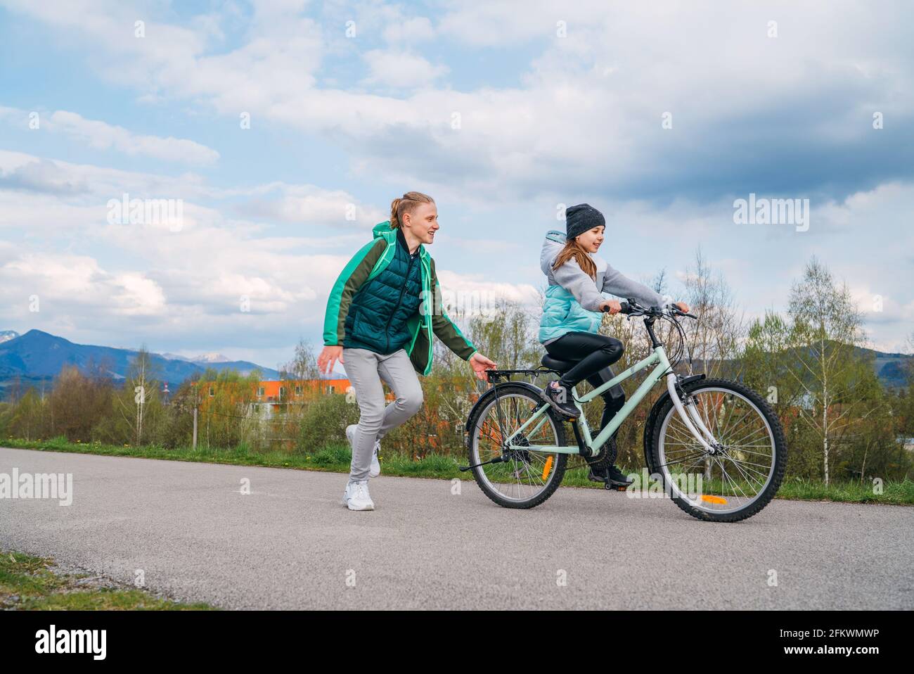 Smiling kids on a bicycle asphalt way. Brother helping to sister and ...