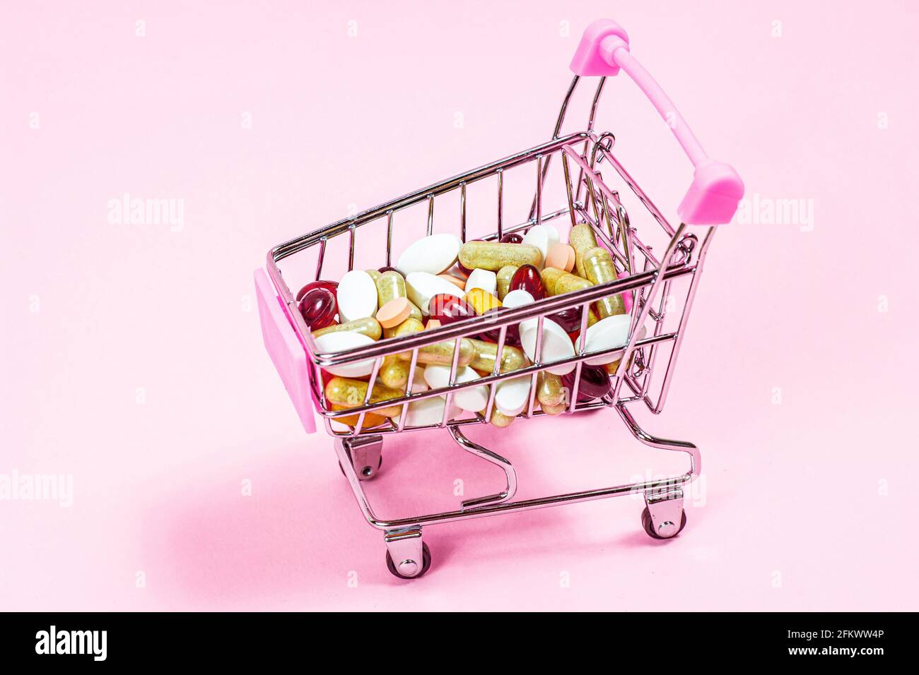 Shopping cart with different medical pills and capsules in it on pink ...
