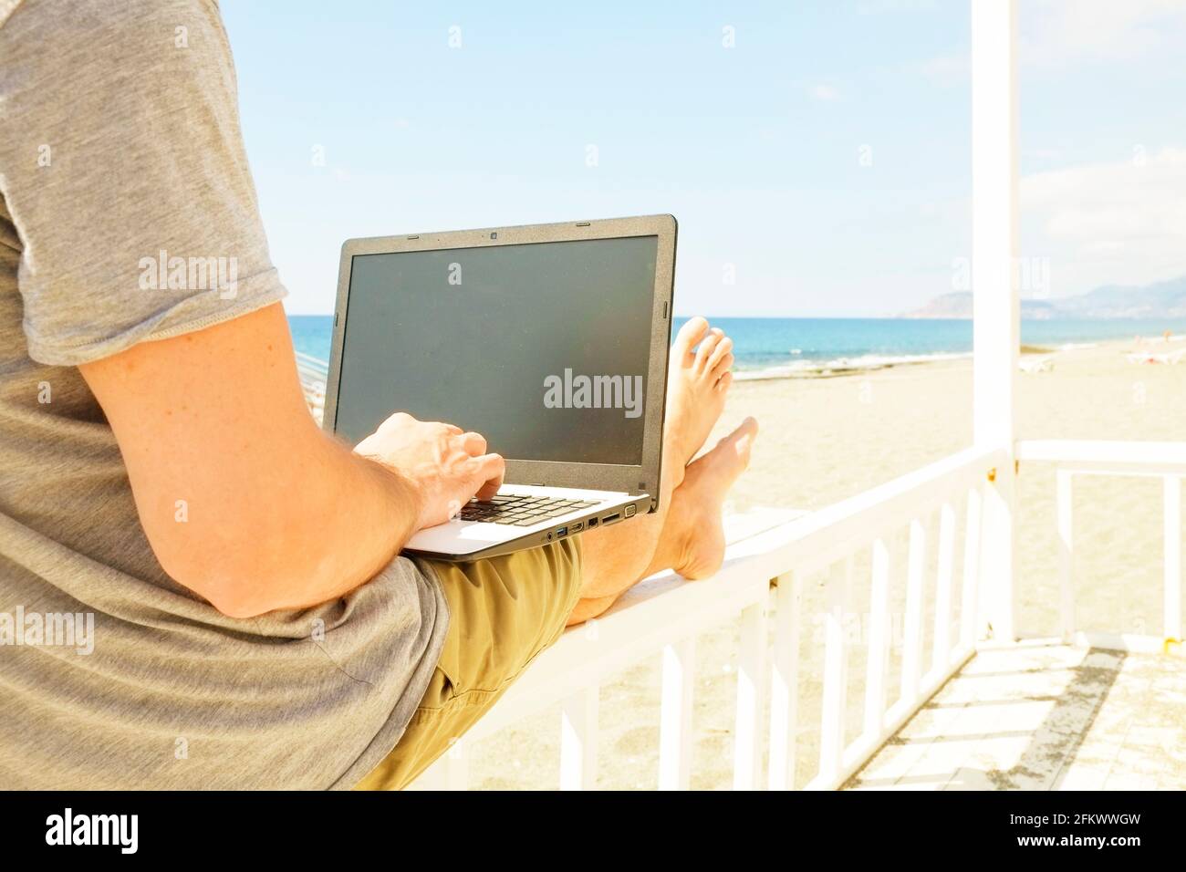 Fit young man using laptop sitting on white wood beach veranda porch ...