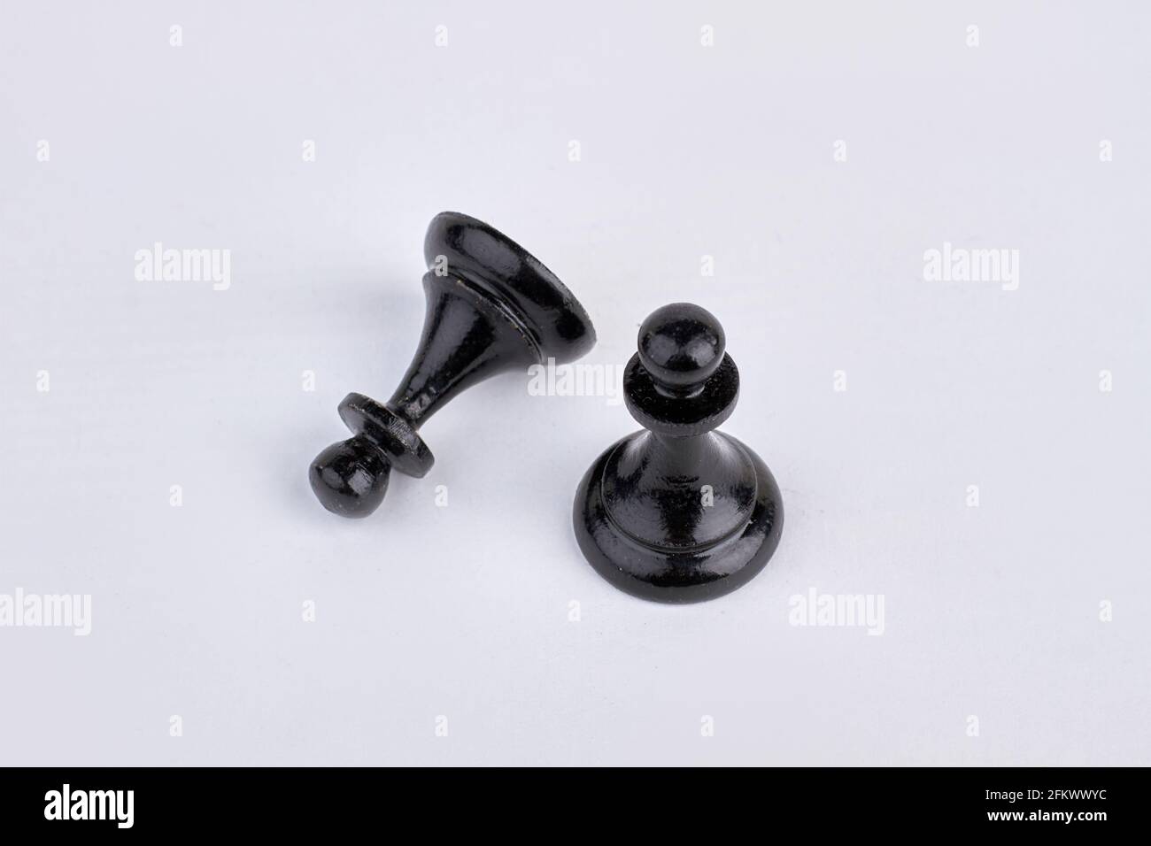 Black pawn chess piece stands near fallen chess piece Stock Photo - Alamy