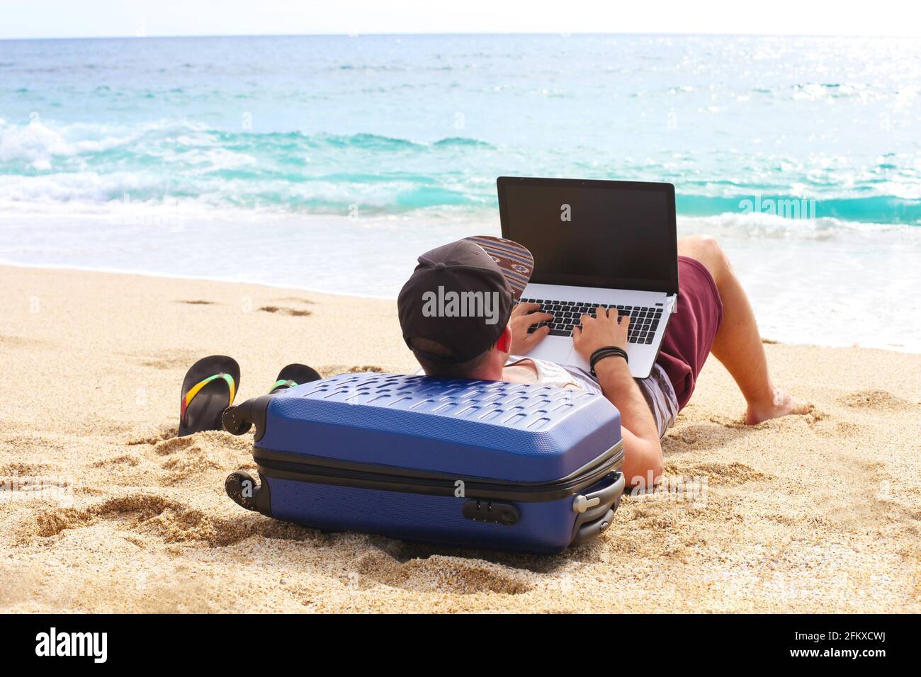 Young man, programmer on sandy beach leaning on suitcase, coding on a ...