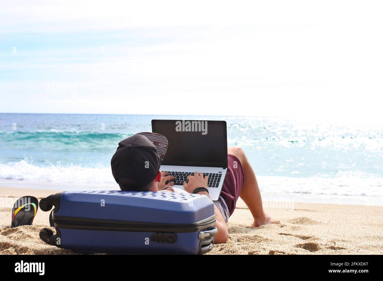 Young man, programmer on sandy beach leaning on suitcase, coding on a ...