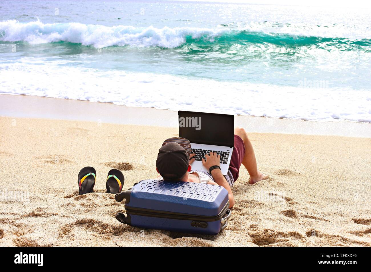 Young man, programmer on sandy beach leaning on suitcase, coding on a ...
