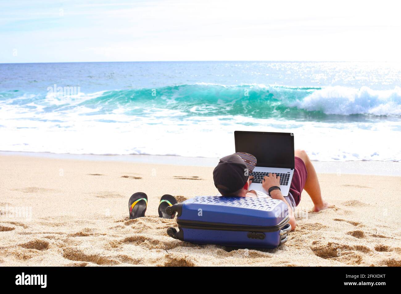 Young man, programmer on sandy beach leaning on suitcase, coding on a ...