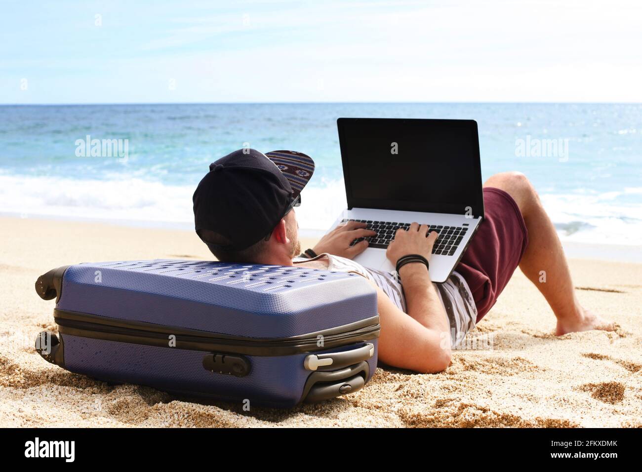 Young man, programmer on sandy beach leaning on suitcase, coding on a ...