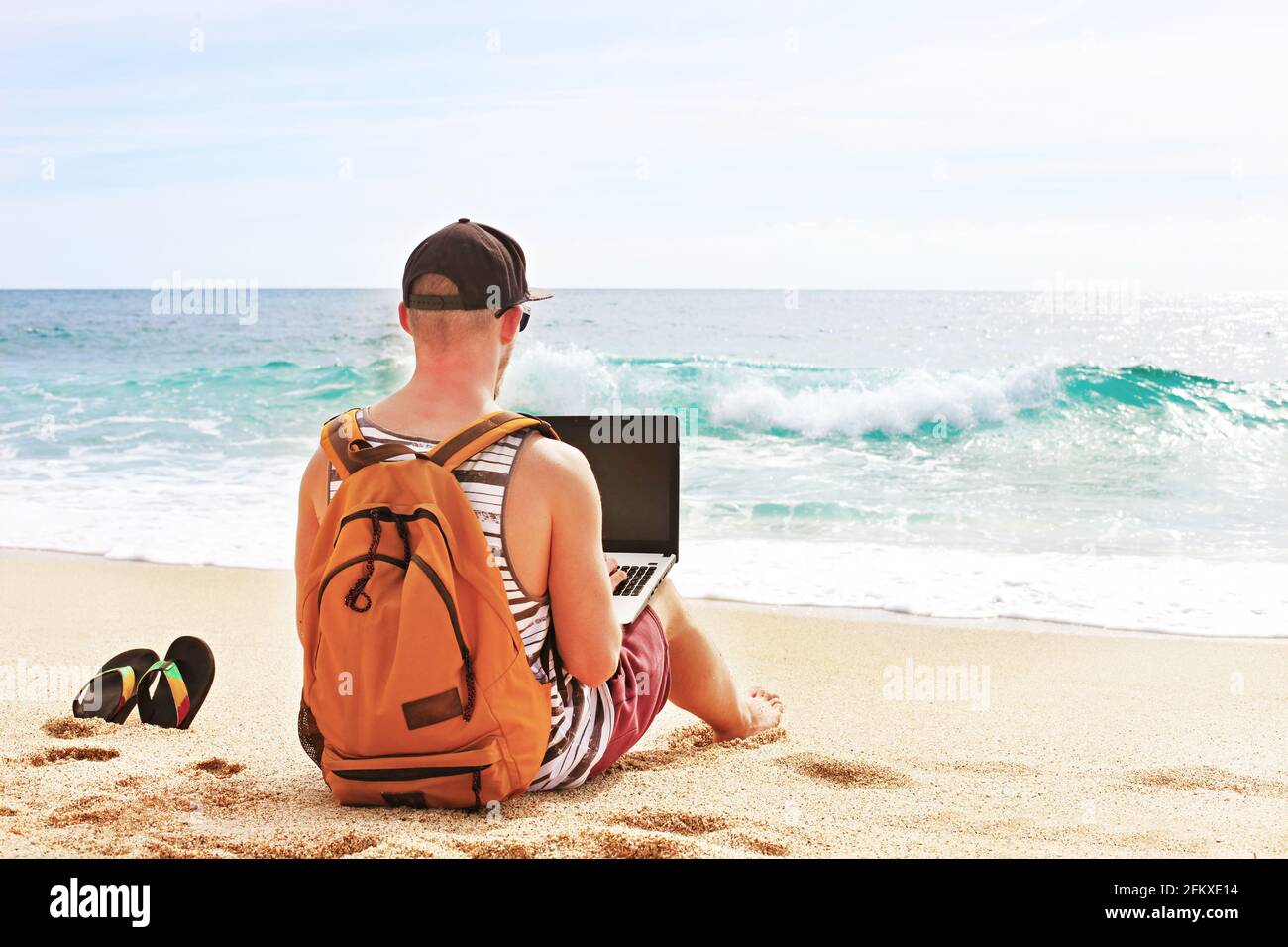 Fit muscle programmer young man sitting on sandy beach, backpack ...