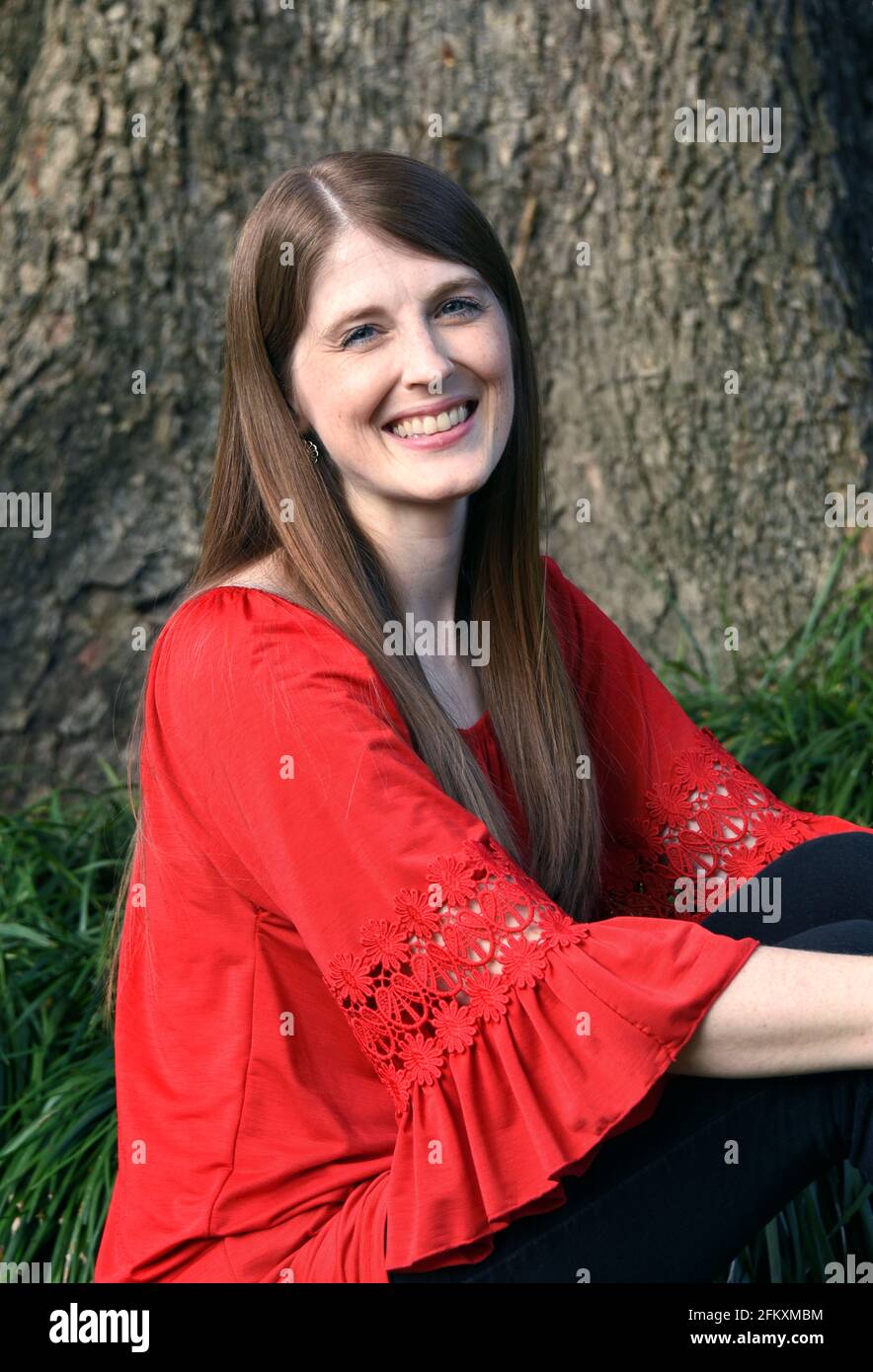 Happy Smile Lights This Young Womans Face She Is Sitting Outsides On The Grass Besides A Tree
