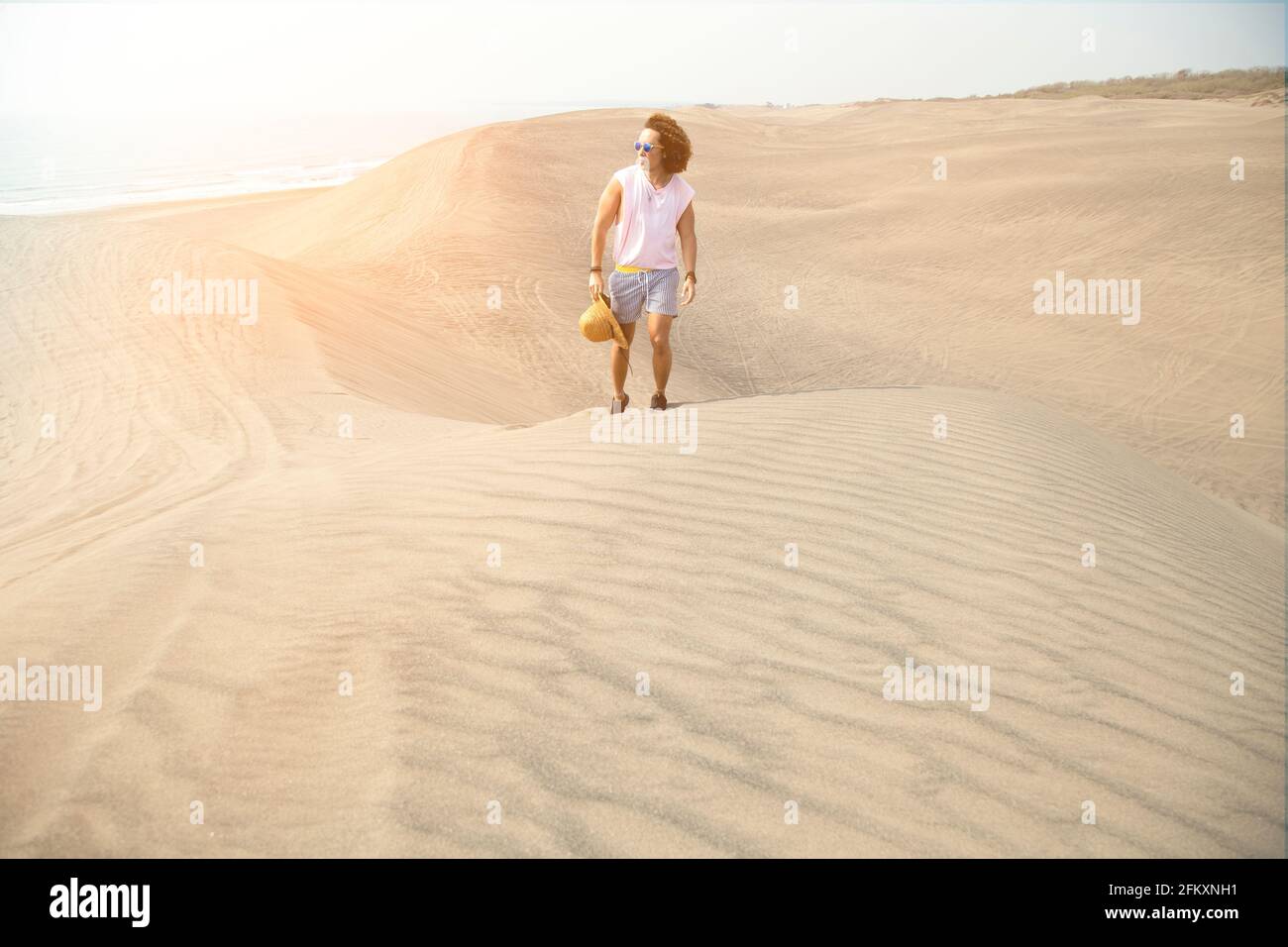 Young male with curly hair, walking on sand dunes during golden hour ...