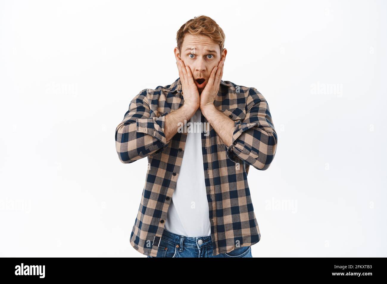Shocked and concerned redhead man gasping, holding hands on face and ...