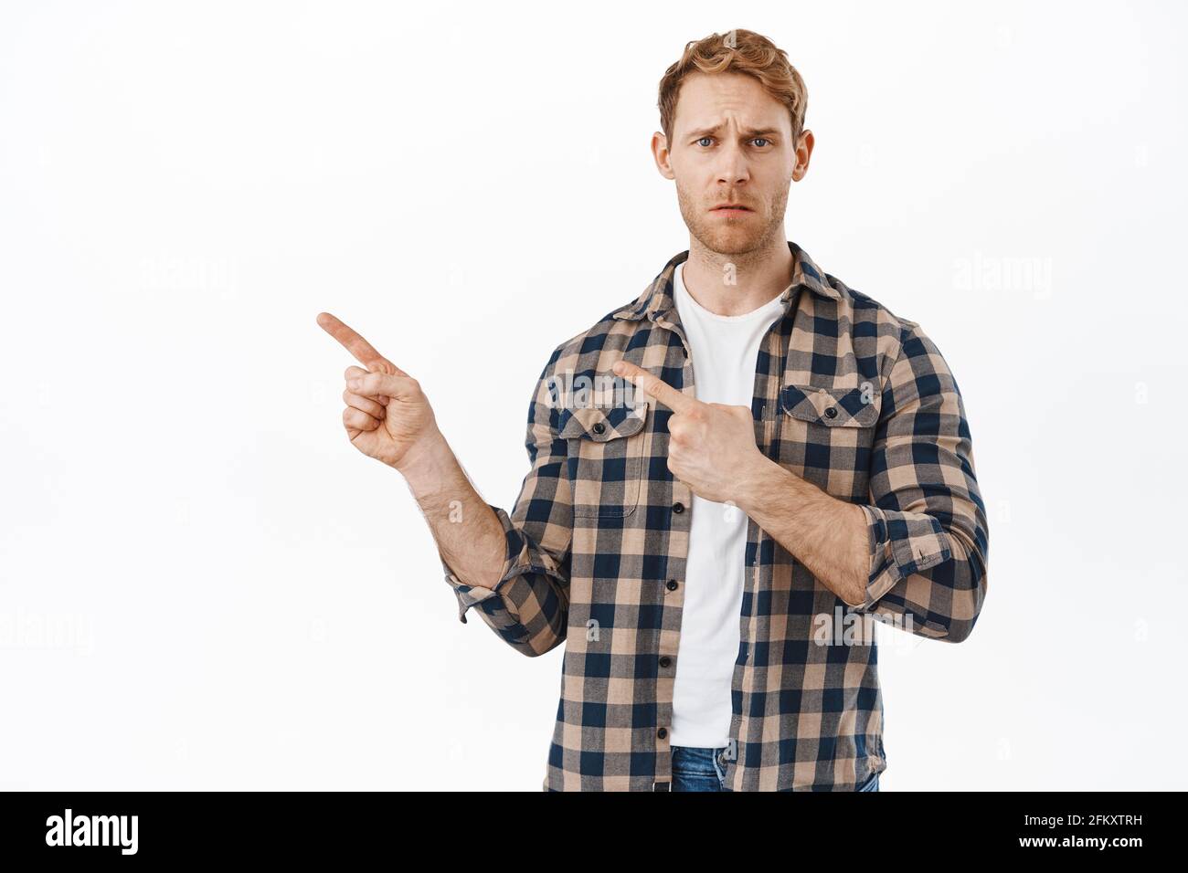 Sad and disappointed redhead man frowning, pointing fingers left with ...