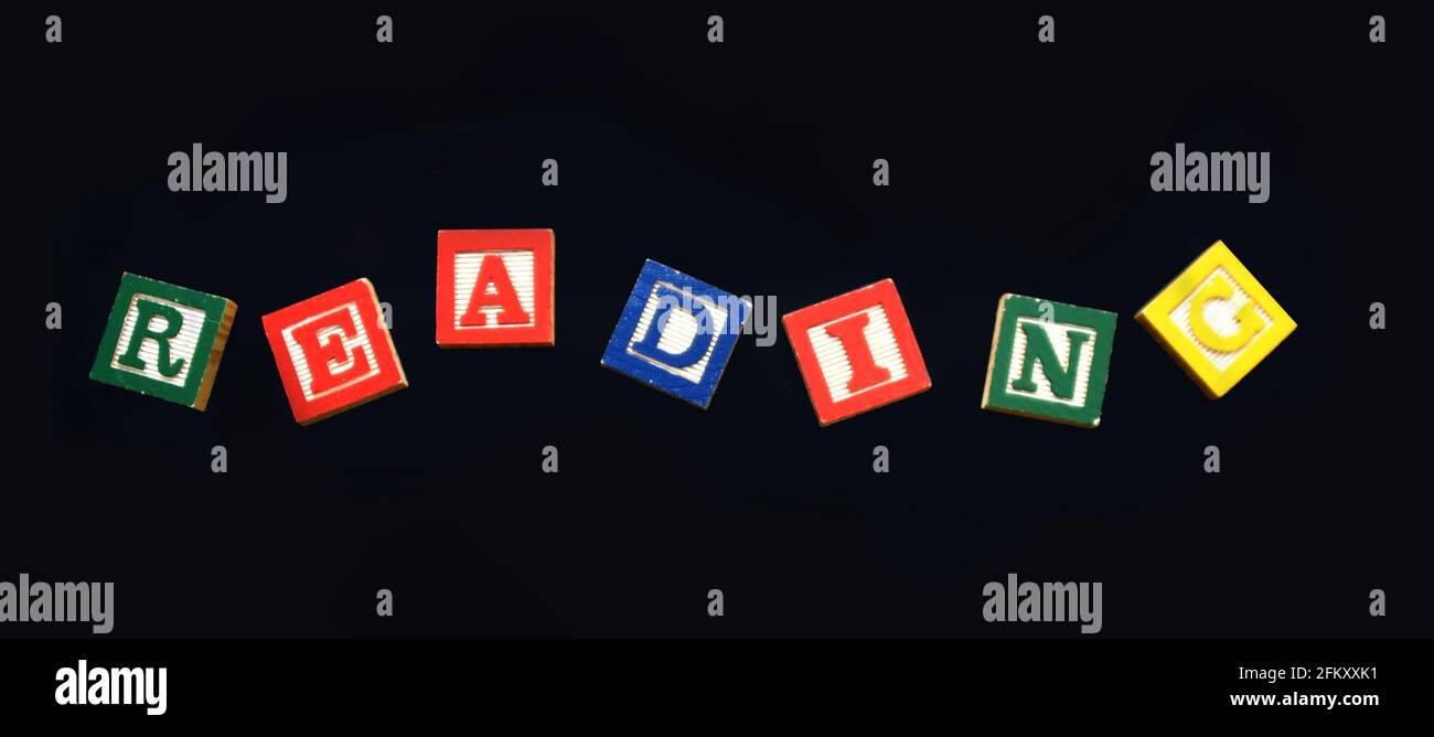 Colorful wooden, block letters spell the word reading. Background is ...