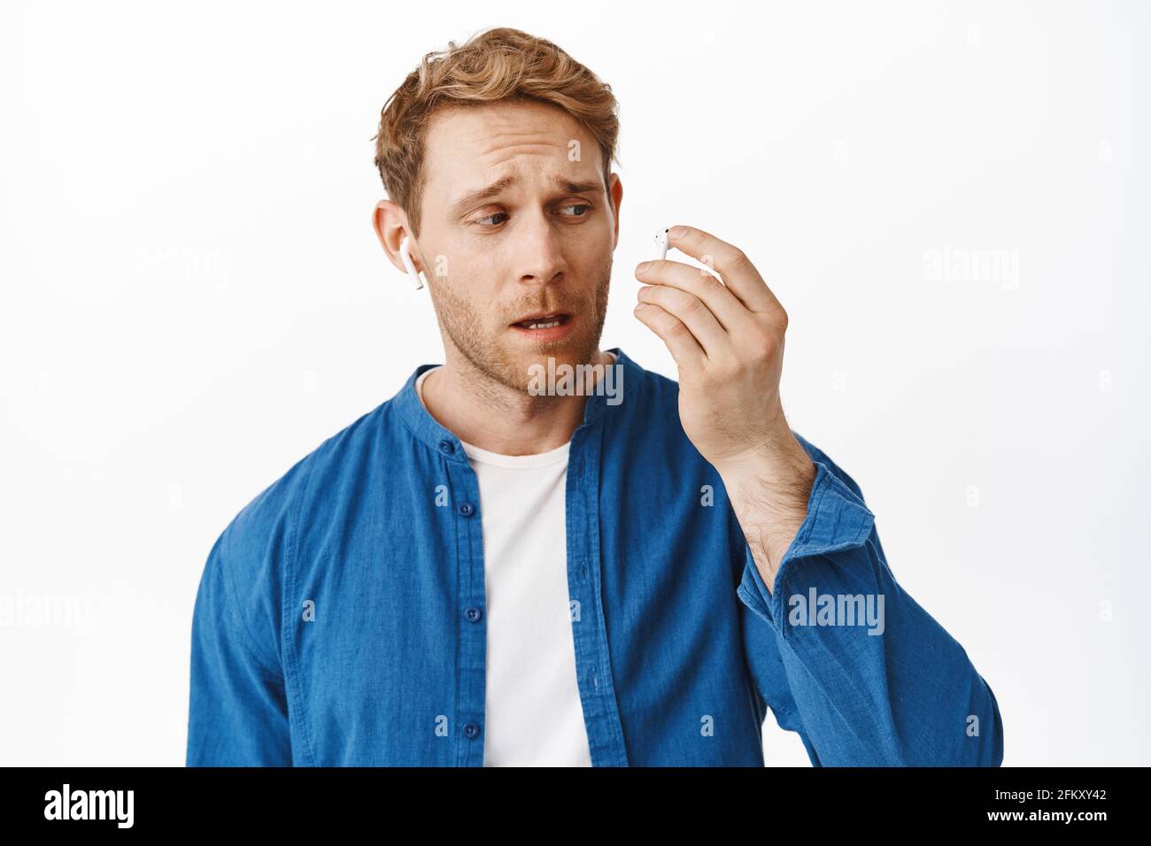 Man looks confused on wireless earphone, broken earbud while listening ...