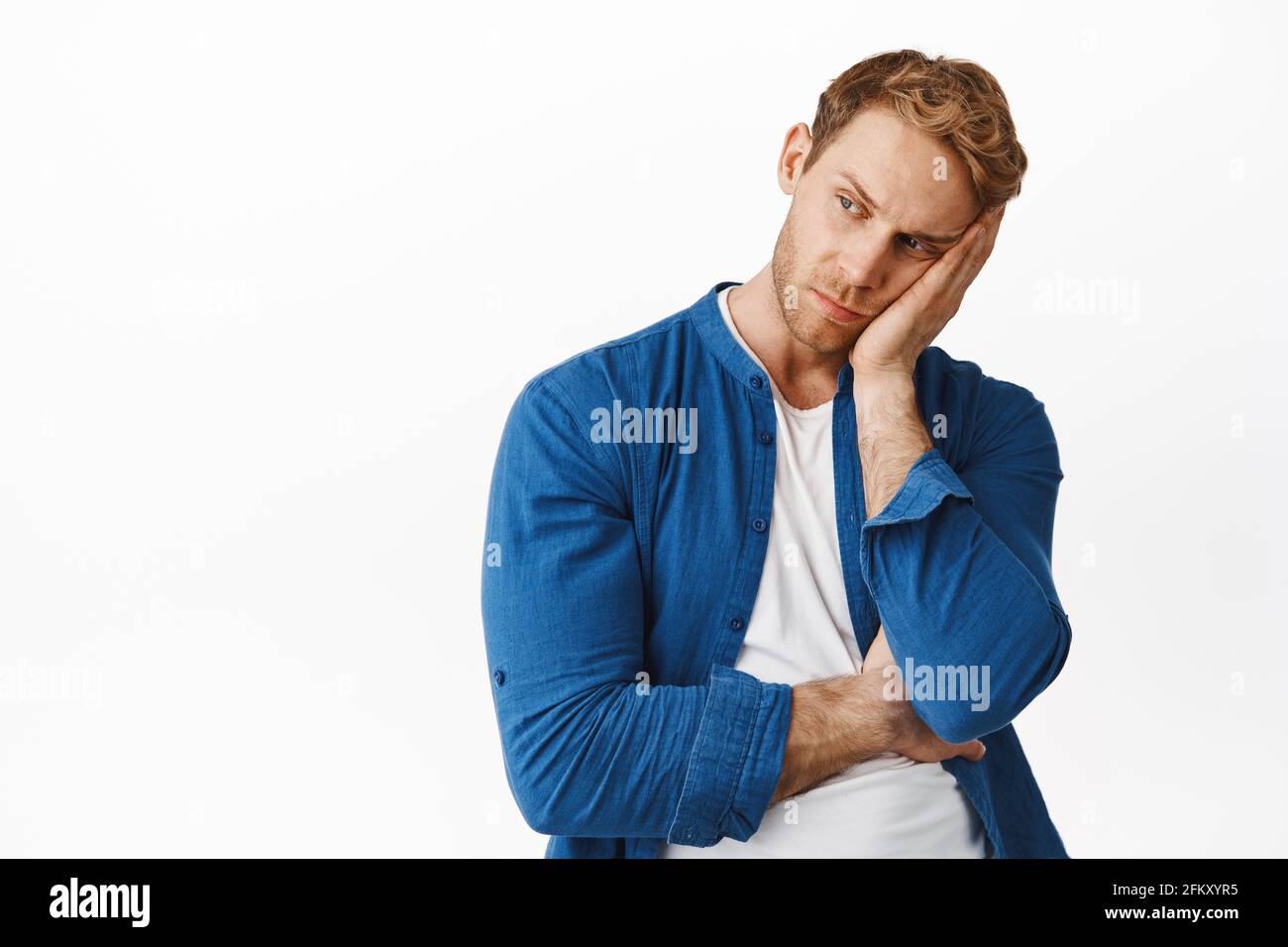 Gloomy and bored young redhead man, lean head on hand, looking aside ...