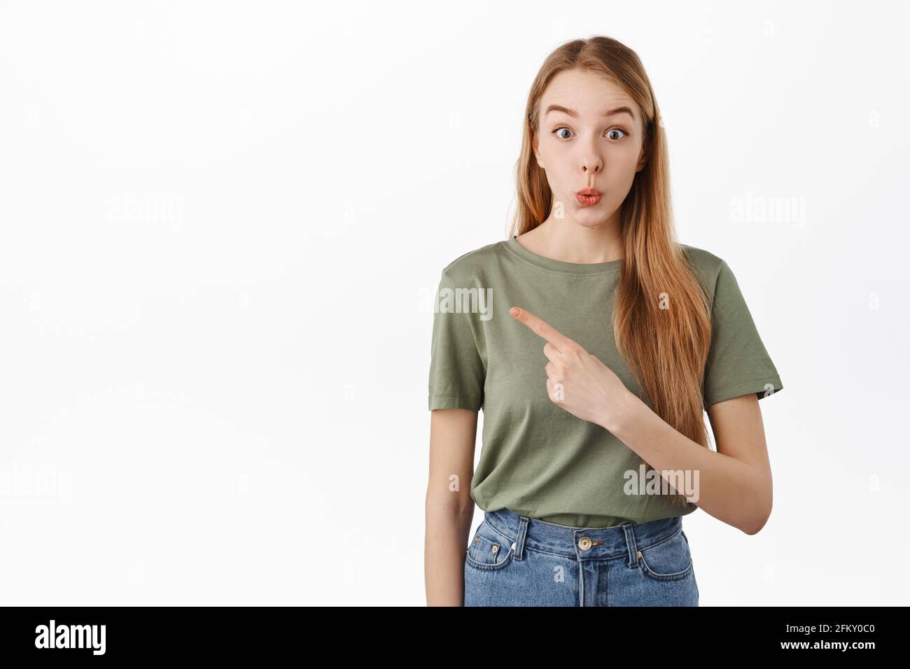 Cute authentic girl looks surprised and intrigued while points left ...