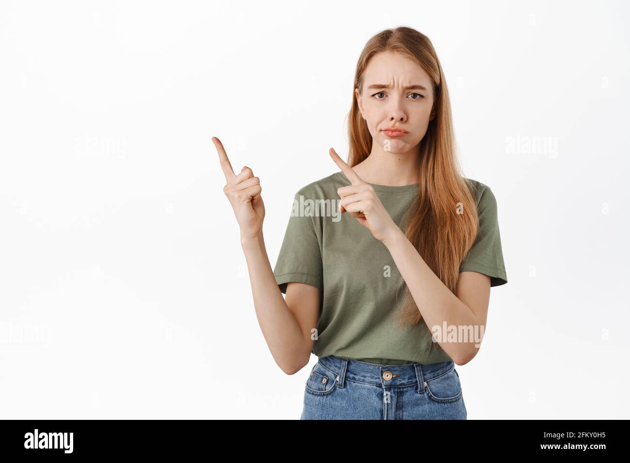 Skeptical young woman looks disappointed and gloomy, smirk and frown ...