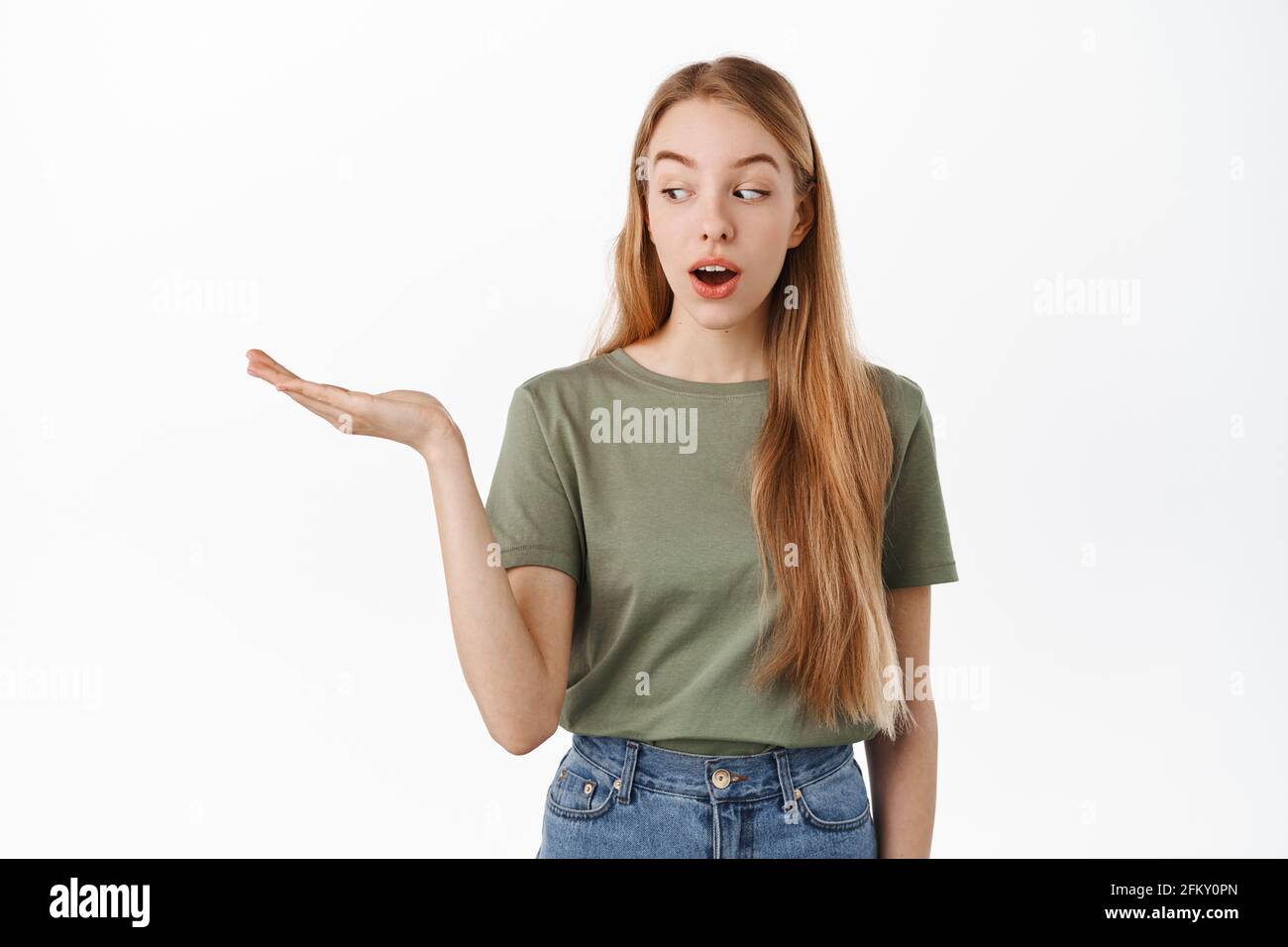 Image of excited girl looks at her hand holding copyspace with interest ...