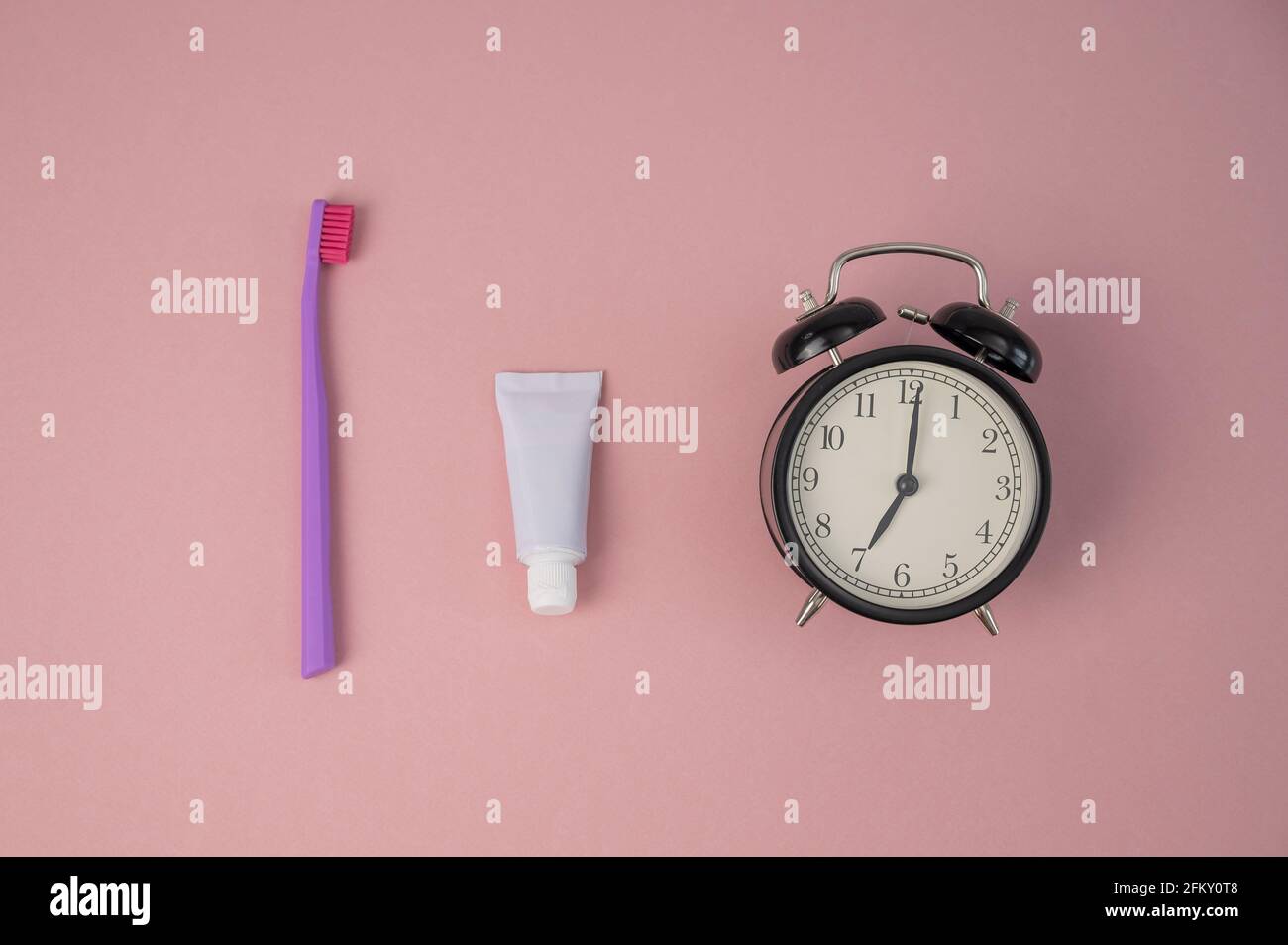 Toothbrush, tube of toothpaste and alarm clock on a pink background ...