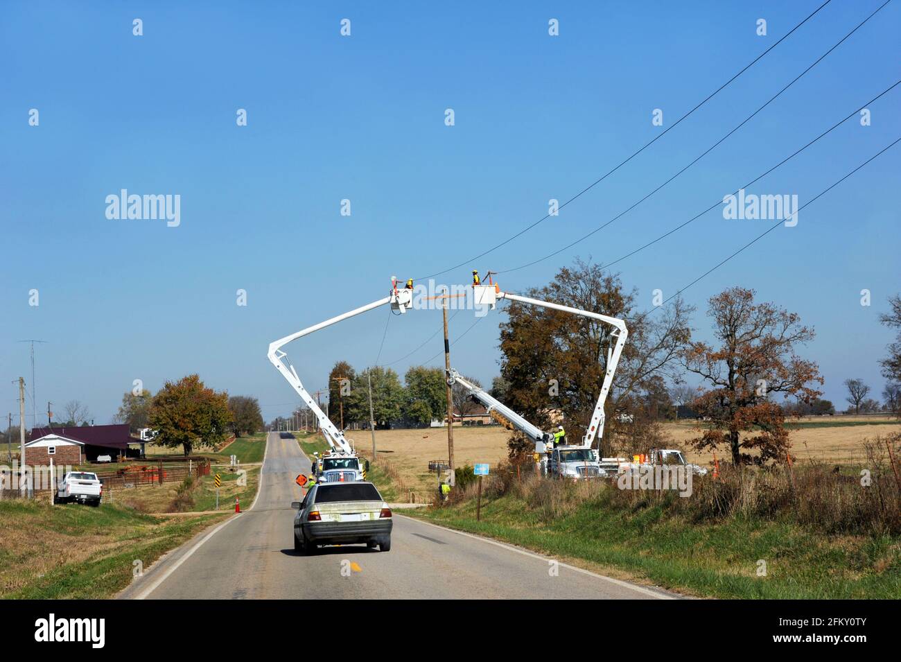 Two linemen stand in cherry pickers working on telephone lines in rural ...