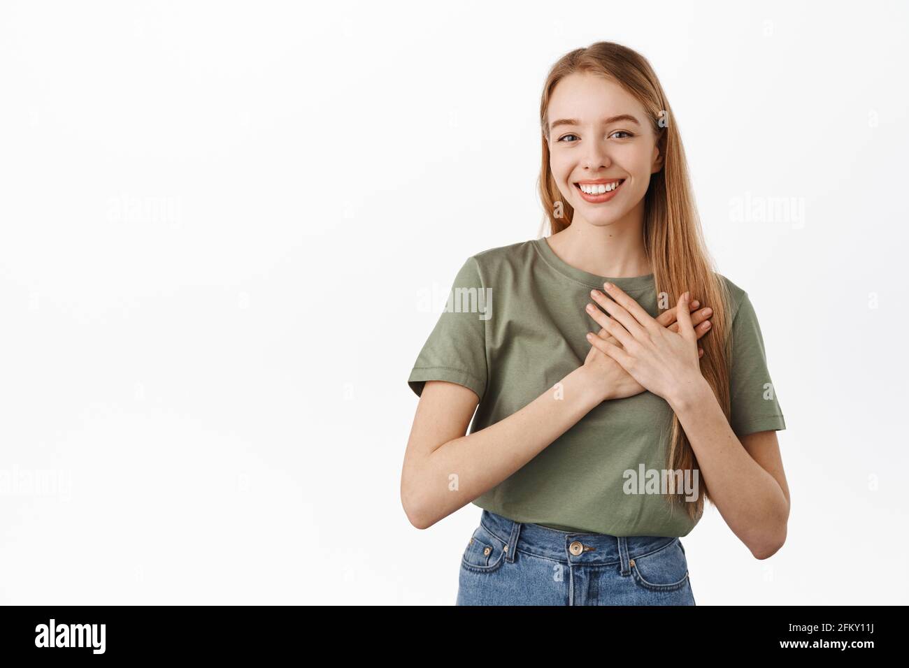 Image of beautiful young woman holding hands on heart, smiling and ...