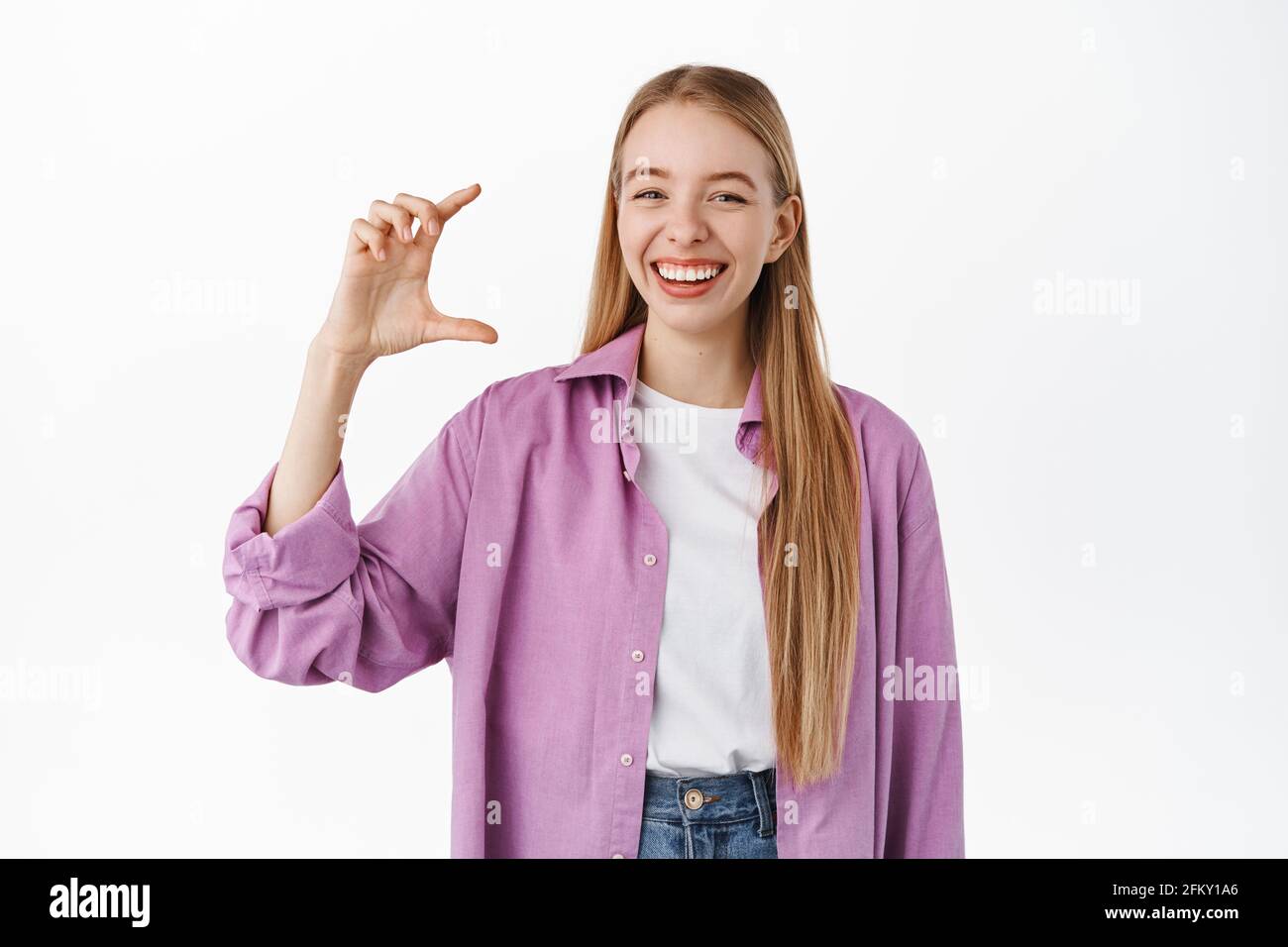 Happy blond girl student showing small size, little thing hand gesture ...