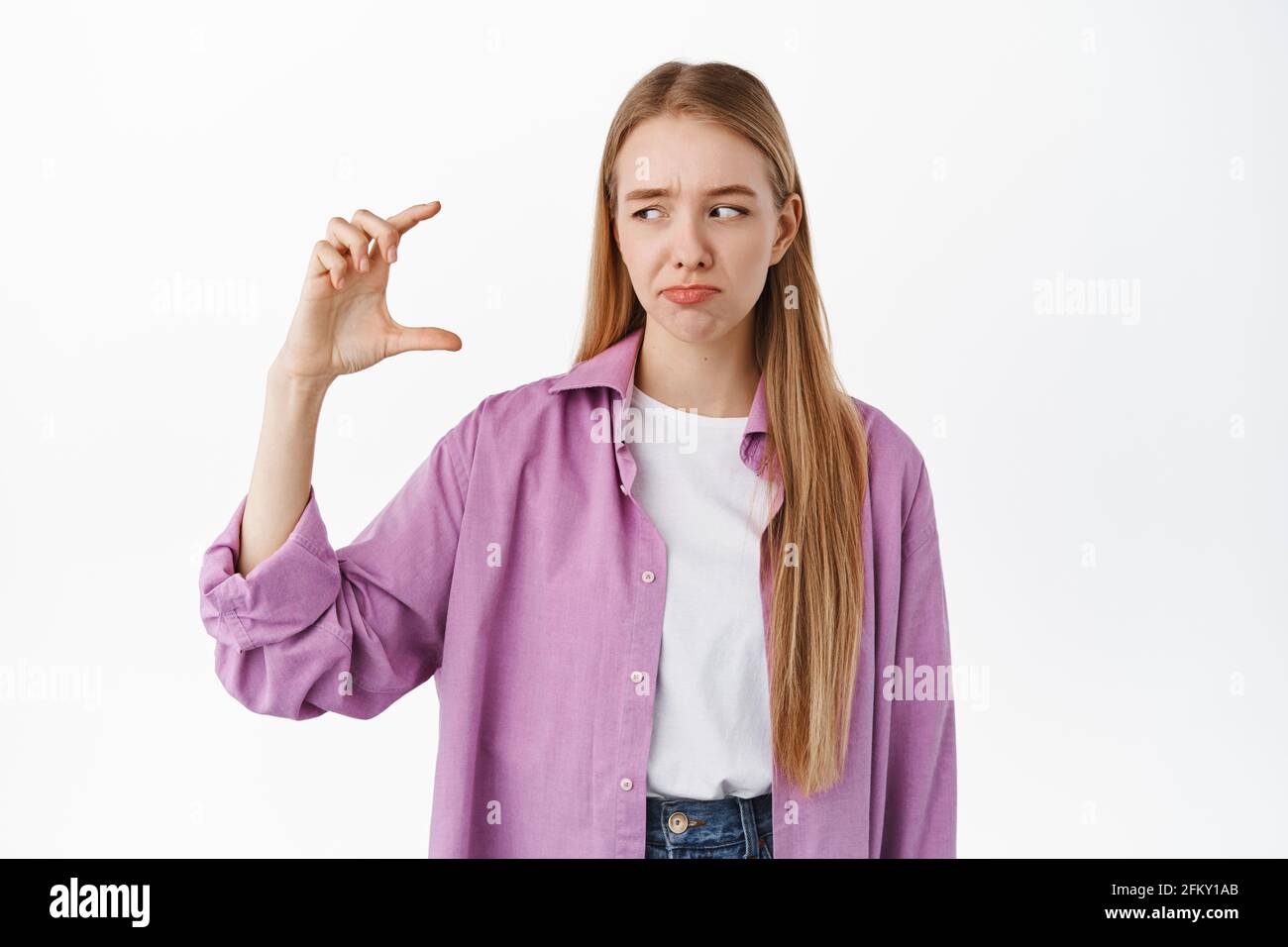 Skeptical young woman looking at her hand holding small tiny, little ...