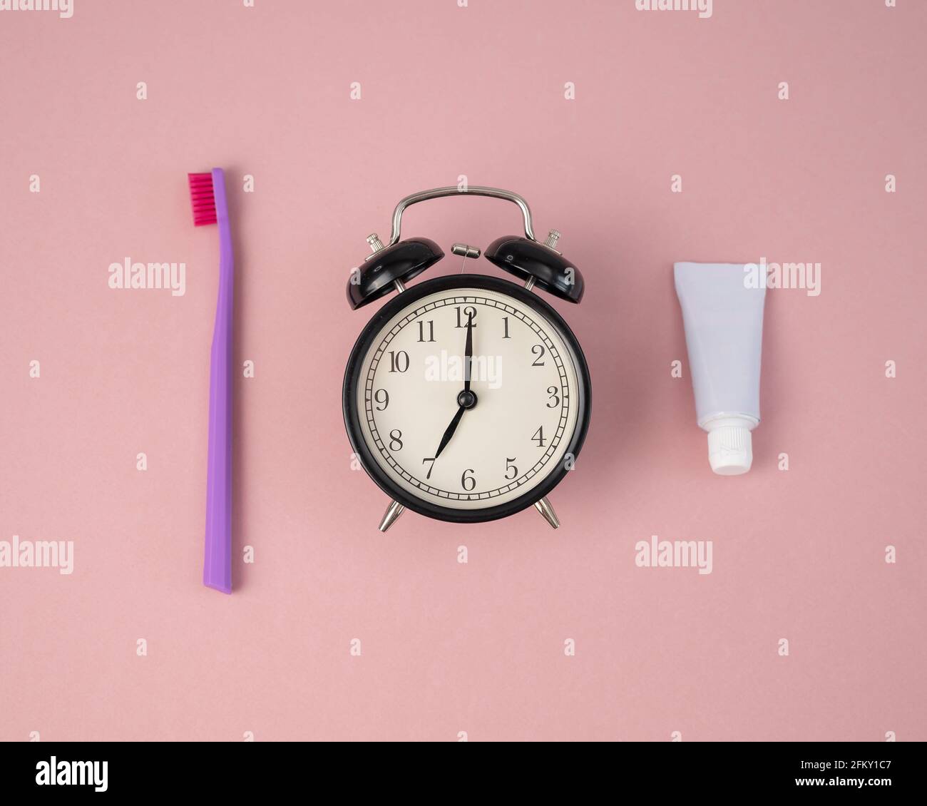 Toothbrush, tube of toothpaste and alarm clock on a pink background ...