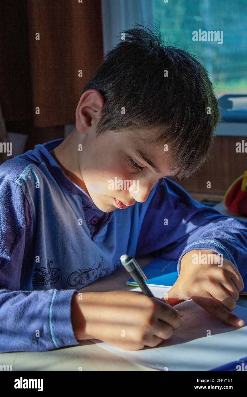 A boy writes his homework with a pen in a notebook, illuminated by ...