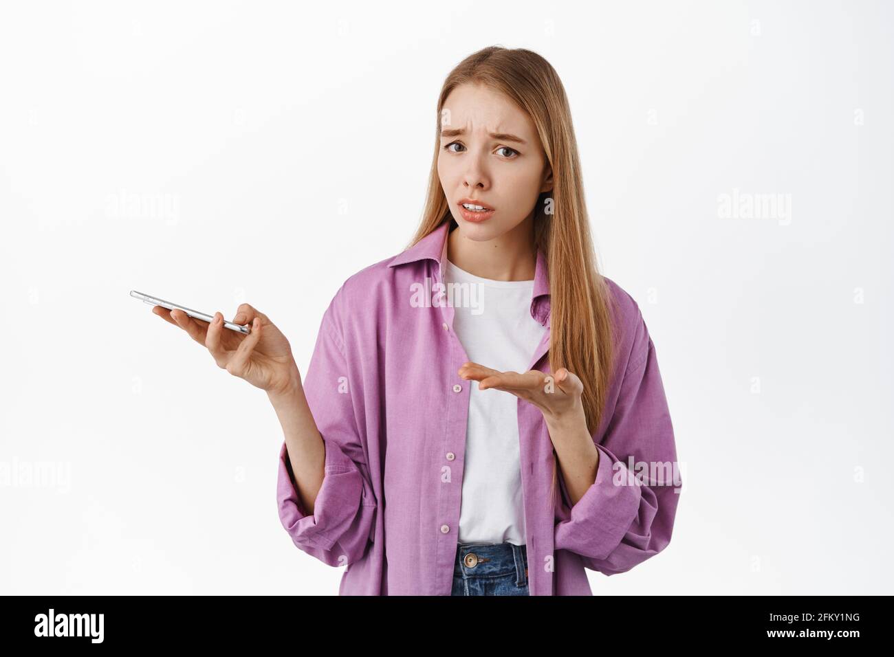 Confused young woman pointing at smartphone and asking question, being ...