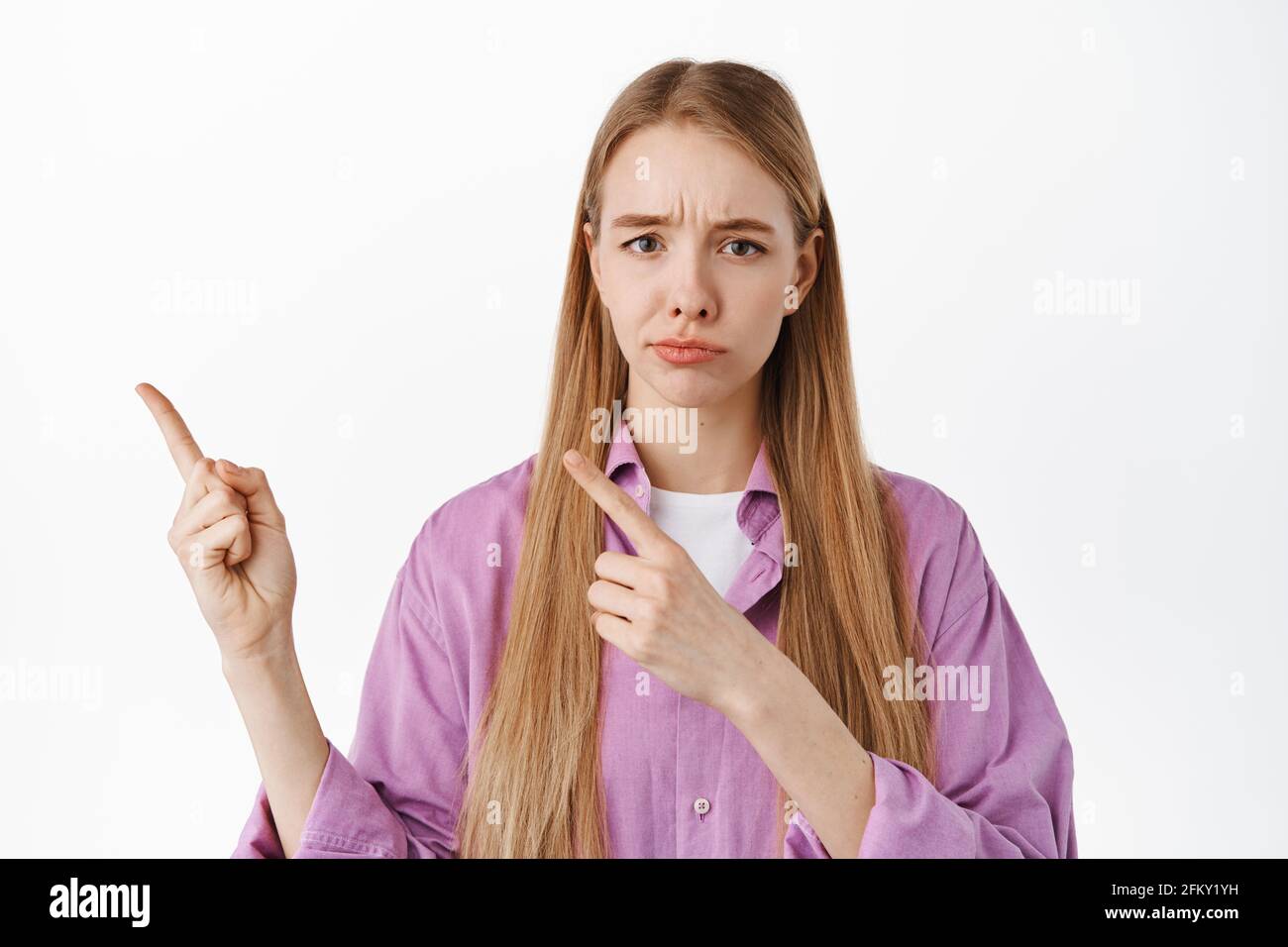 Disappointed young woman points fingers left and complains, dislike ...